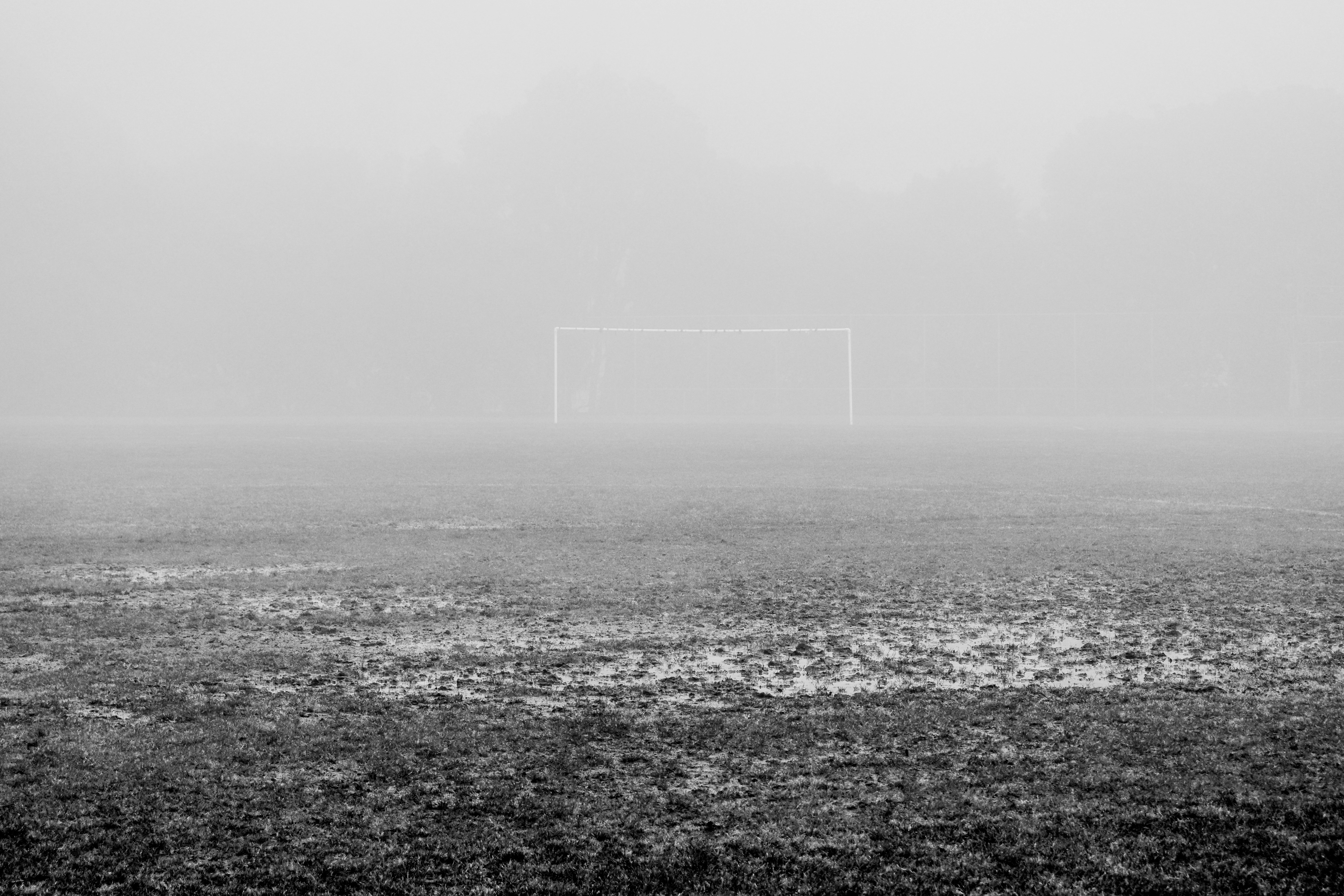A soccer goal at the end of a muddy field during fog | Soccer goal on a foggy field