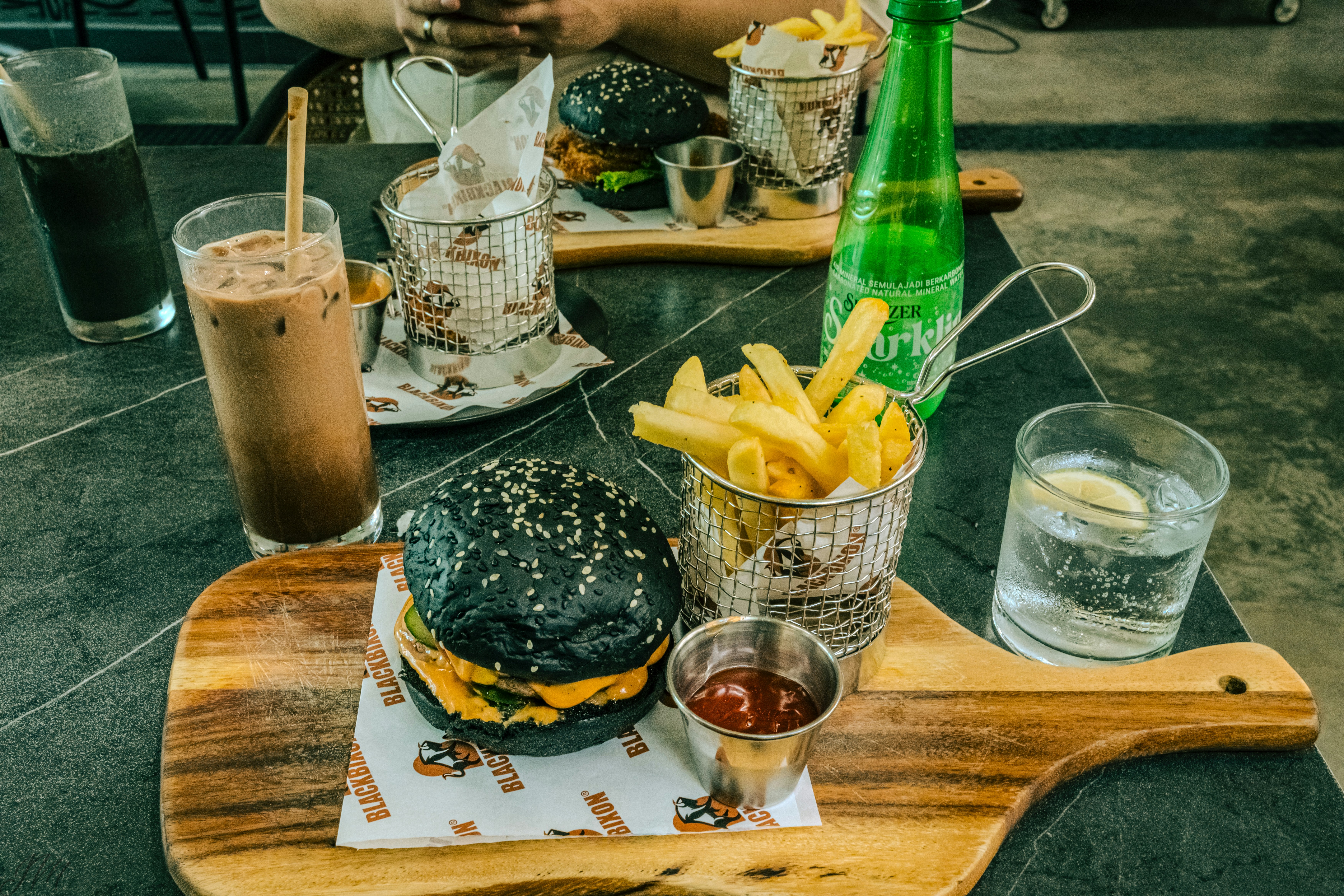 Black burger with fries and drinks on wooden board