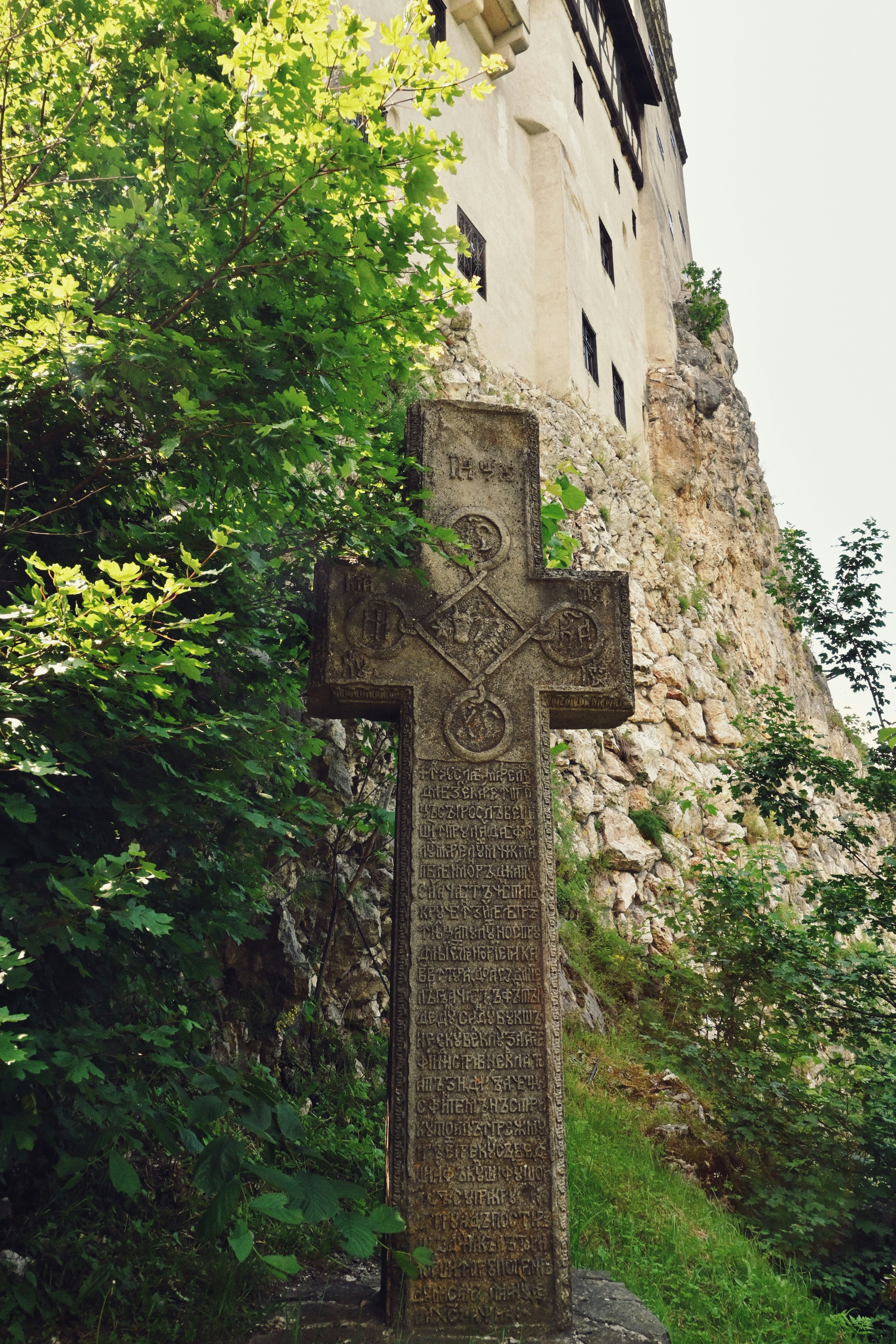 Stone cross stands near castle on rocky hillside