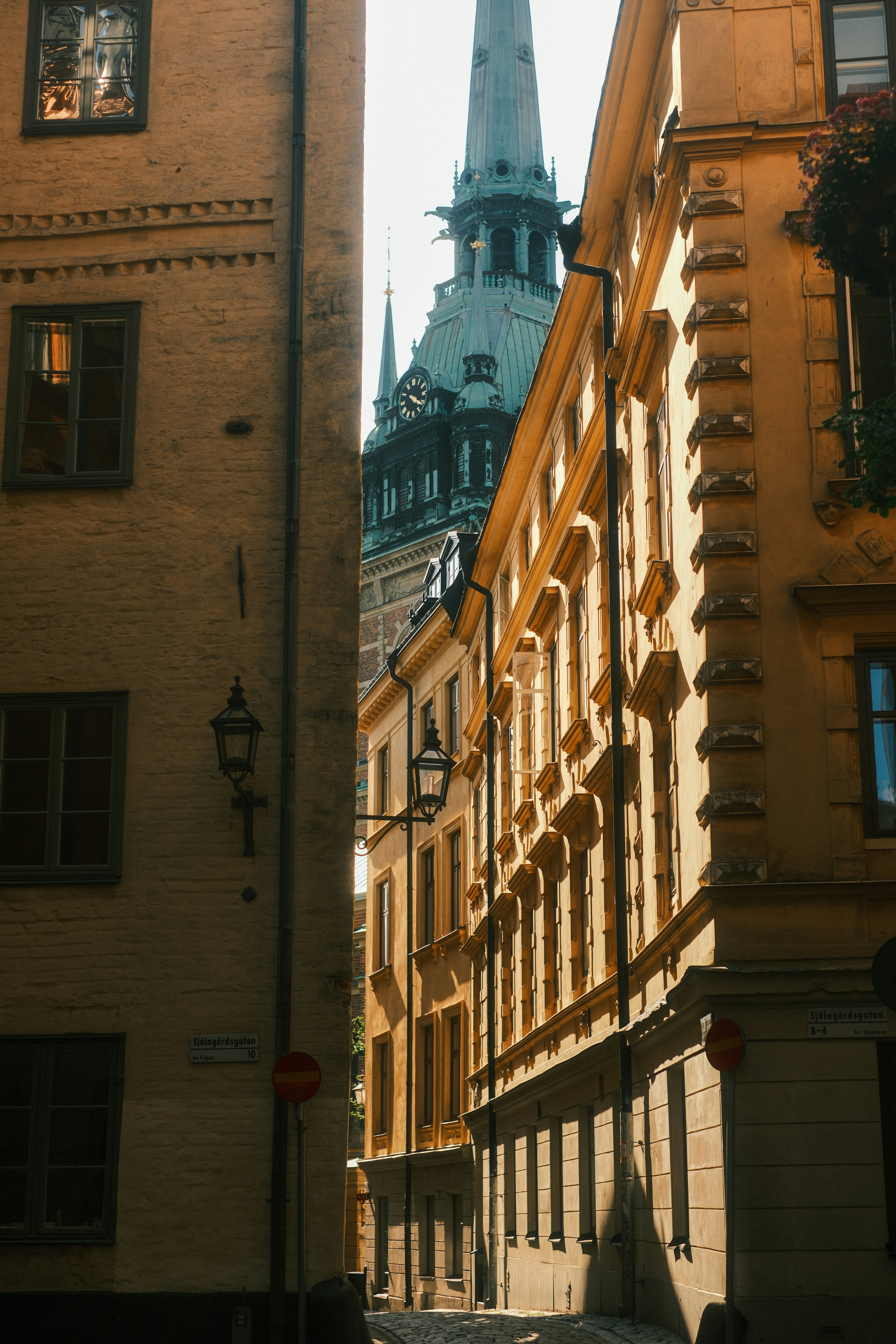 St Gertrude Church visible through the old streets of Gamla Stan, Stockholm, Sweden | Narrow european street with historic buildings and spire.