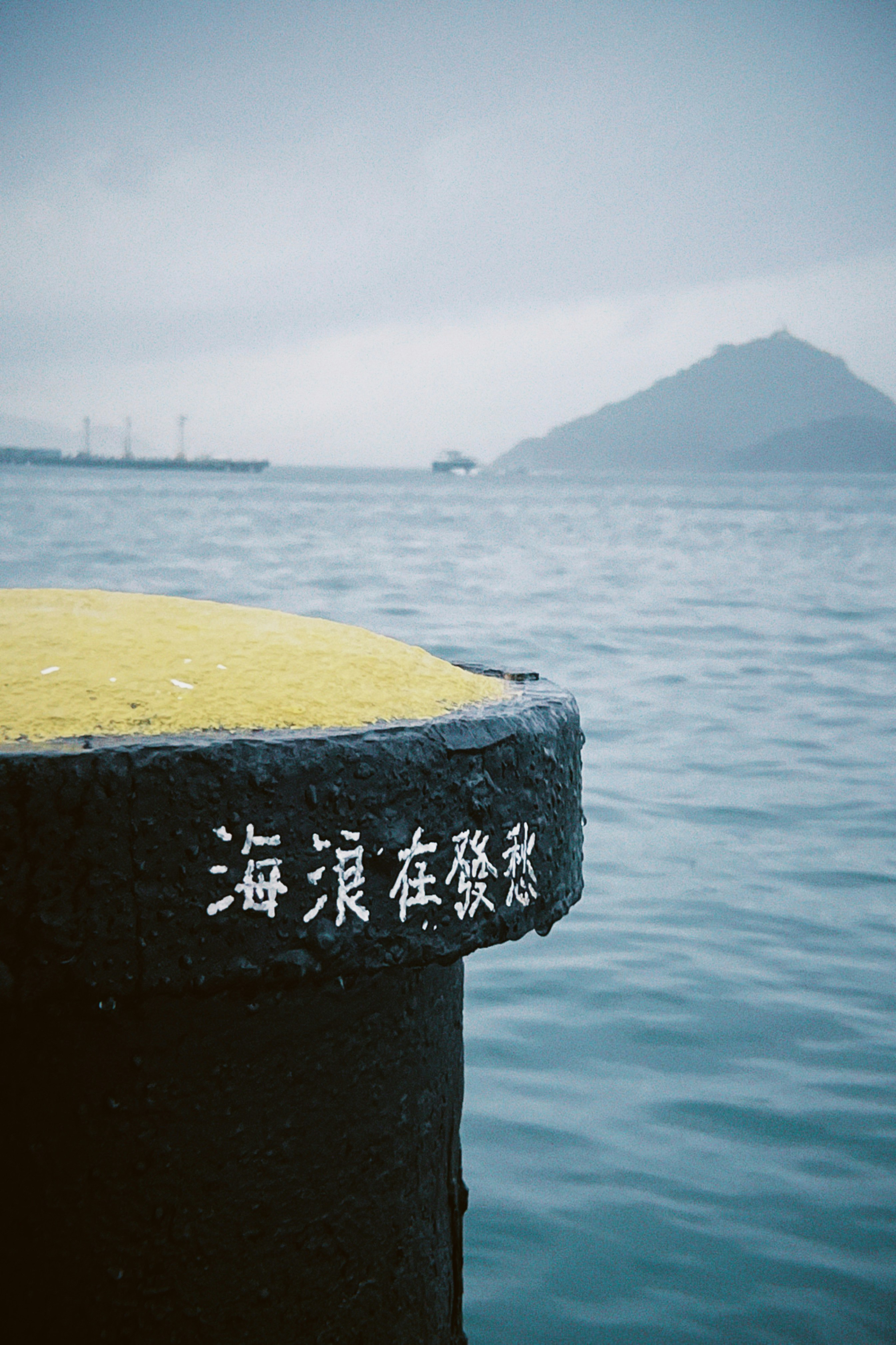 A bollard with chinese text by the water.