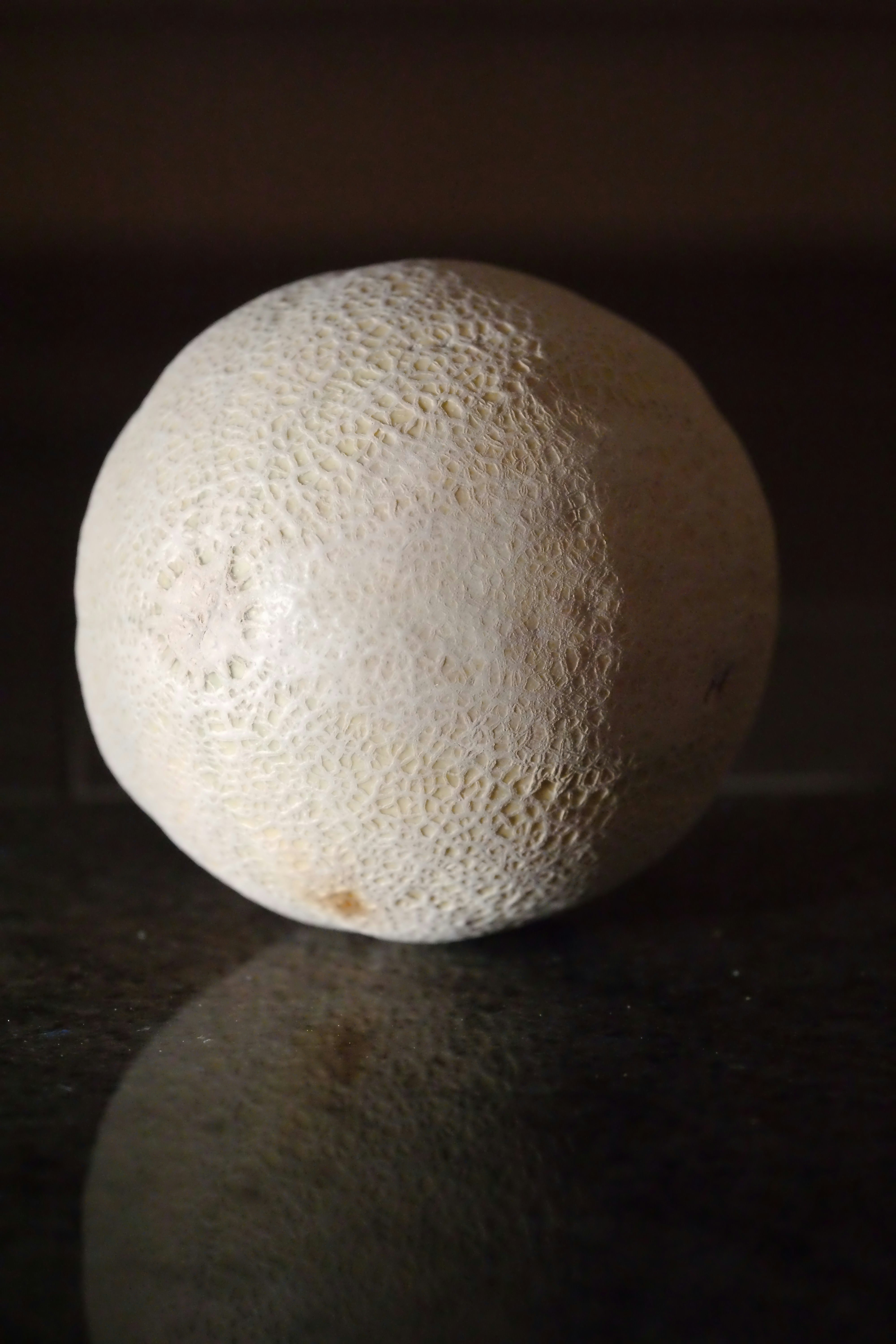 A whole cantaloupe rests on a dark surface.