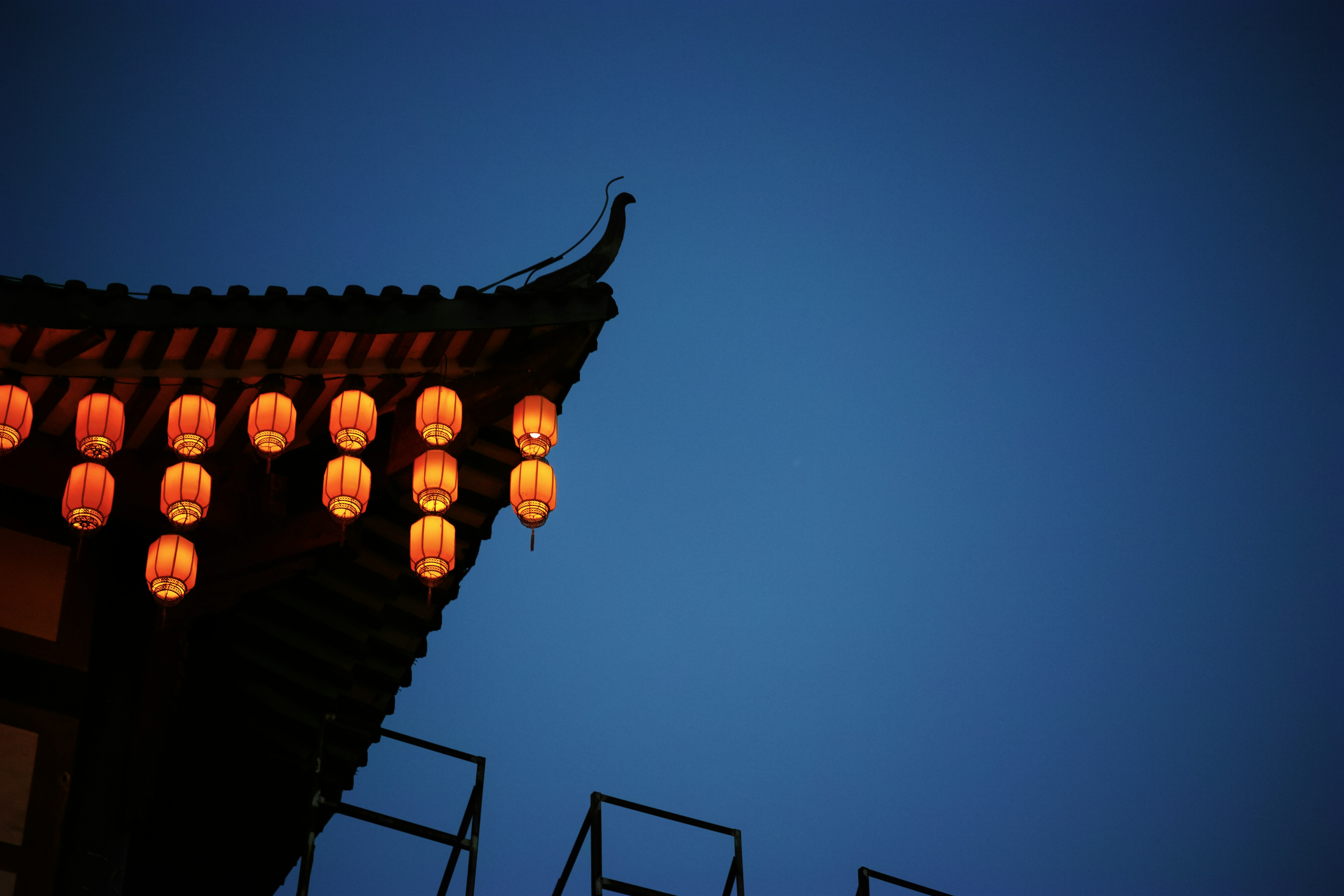 Traditional lanterns illuminate a building roof at dusk.