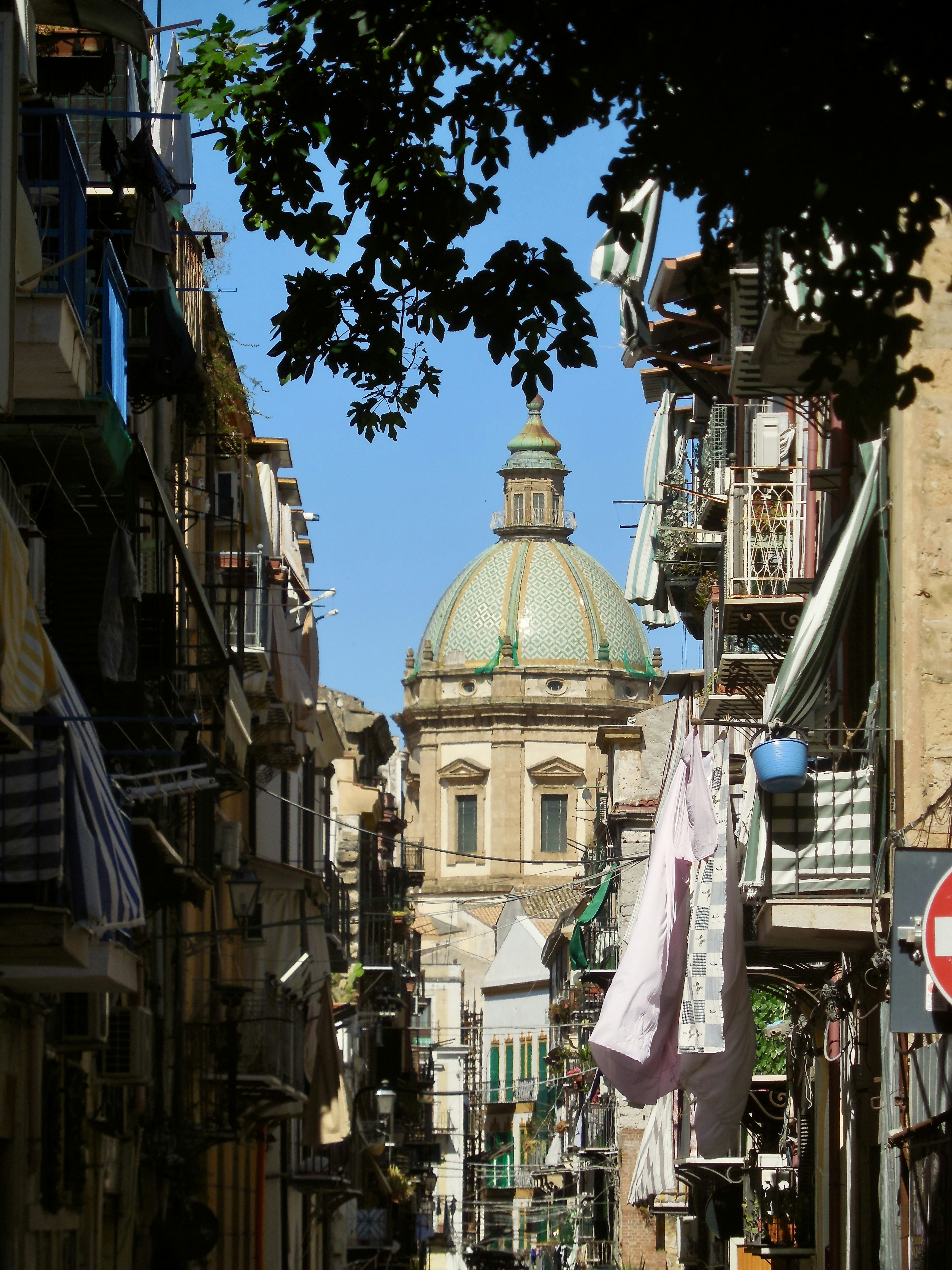 Historic dome peeks through narrow street lined with balconies and laundry. Vibrant urban scene captures the essence of city life.