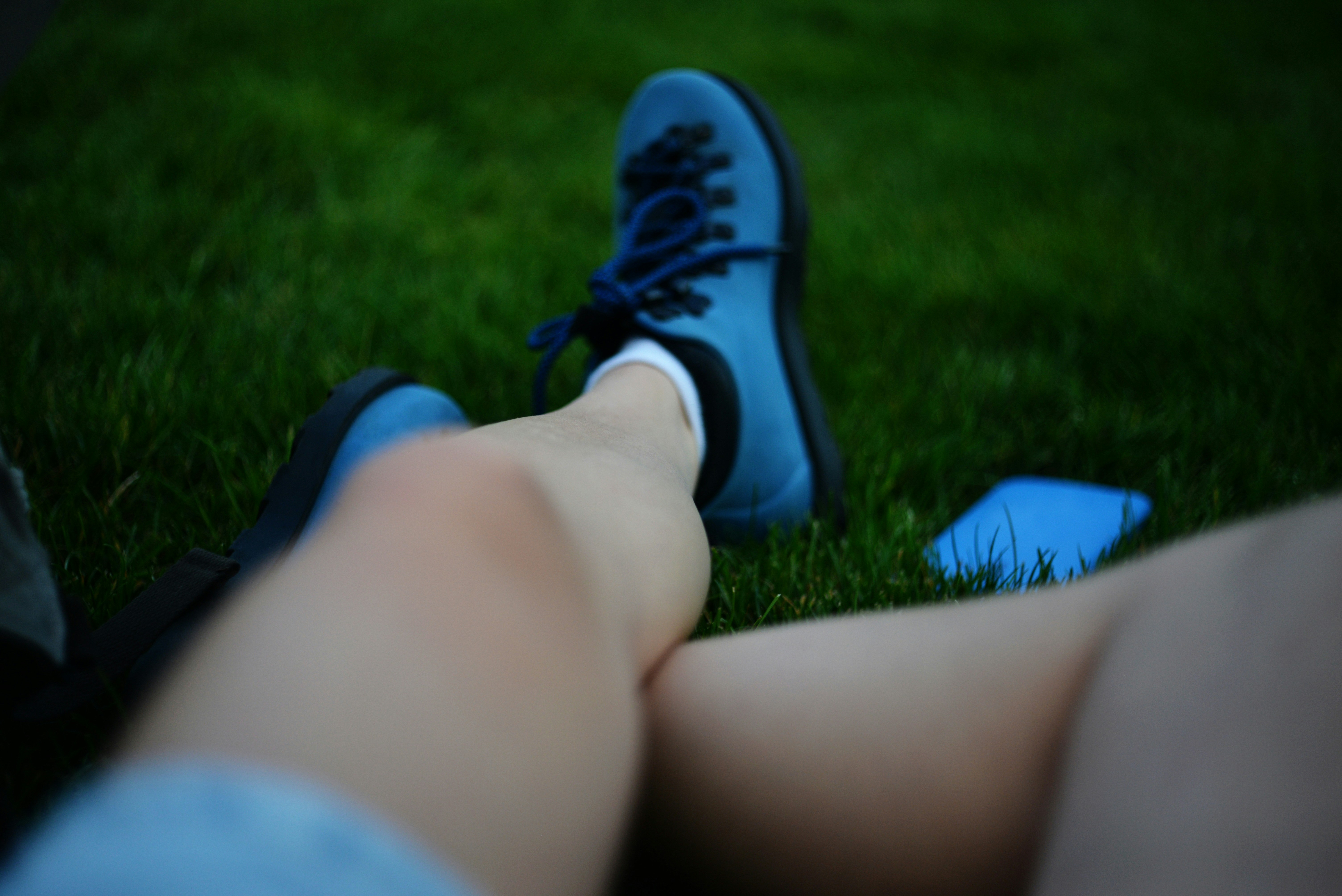 Person wearing blue sneakers sitting on grass