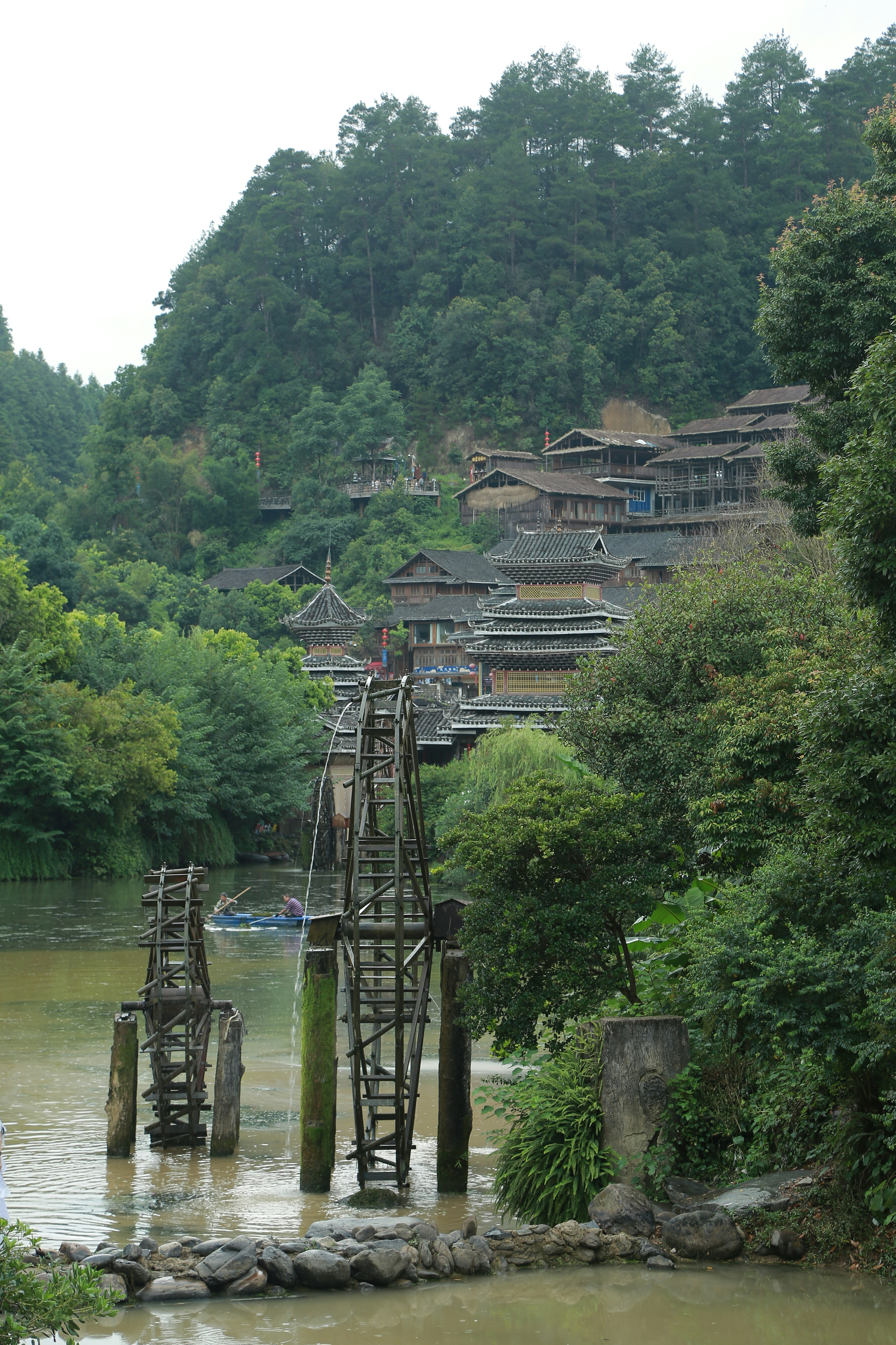 Wooden water wheels on a river near a village.