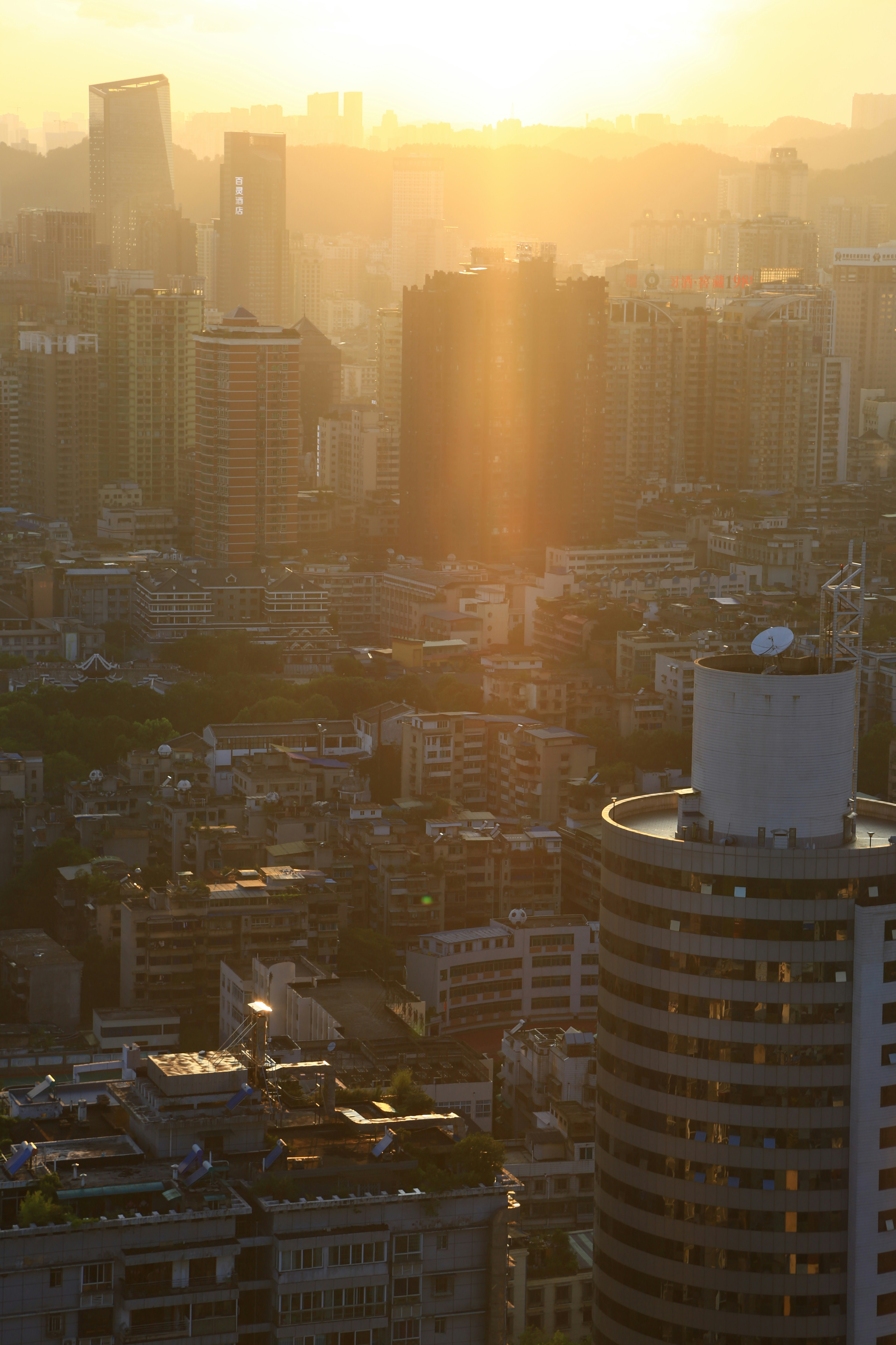 Golden sunbeams illuminate a hazy cityscape at sunset.