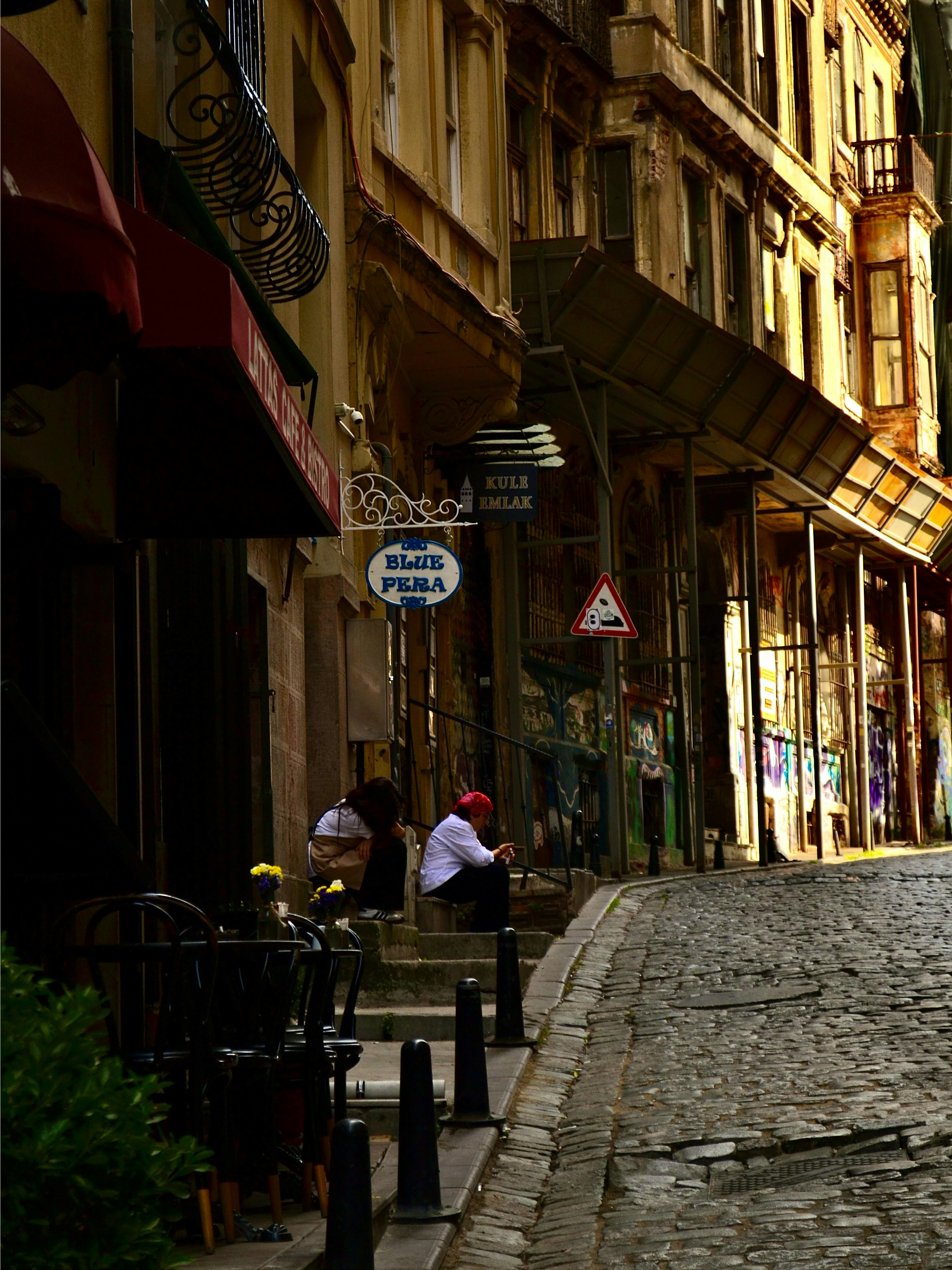 Lonely together | Cobblestone street with old buildings and people sitting.