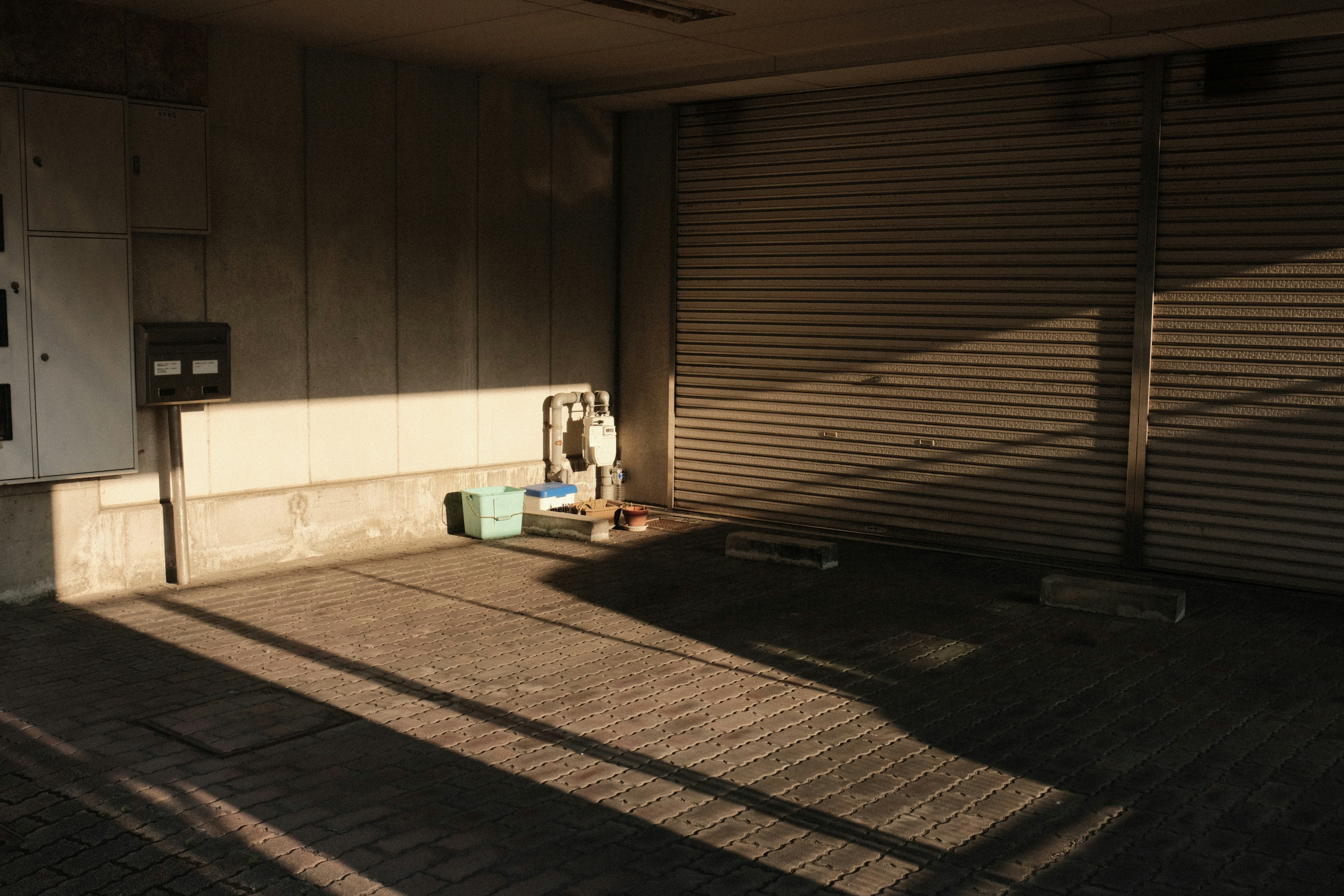 A deserted parking space illuminated by soft afternoon light, featuring a utility box and scattered items on the ground. The scene evokes a sense of stillness and forgotten stories.