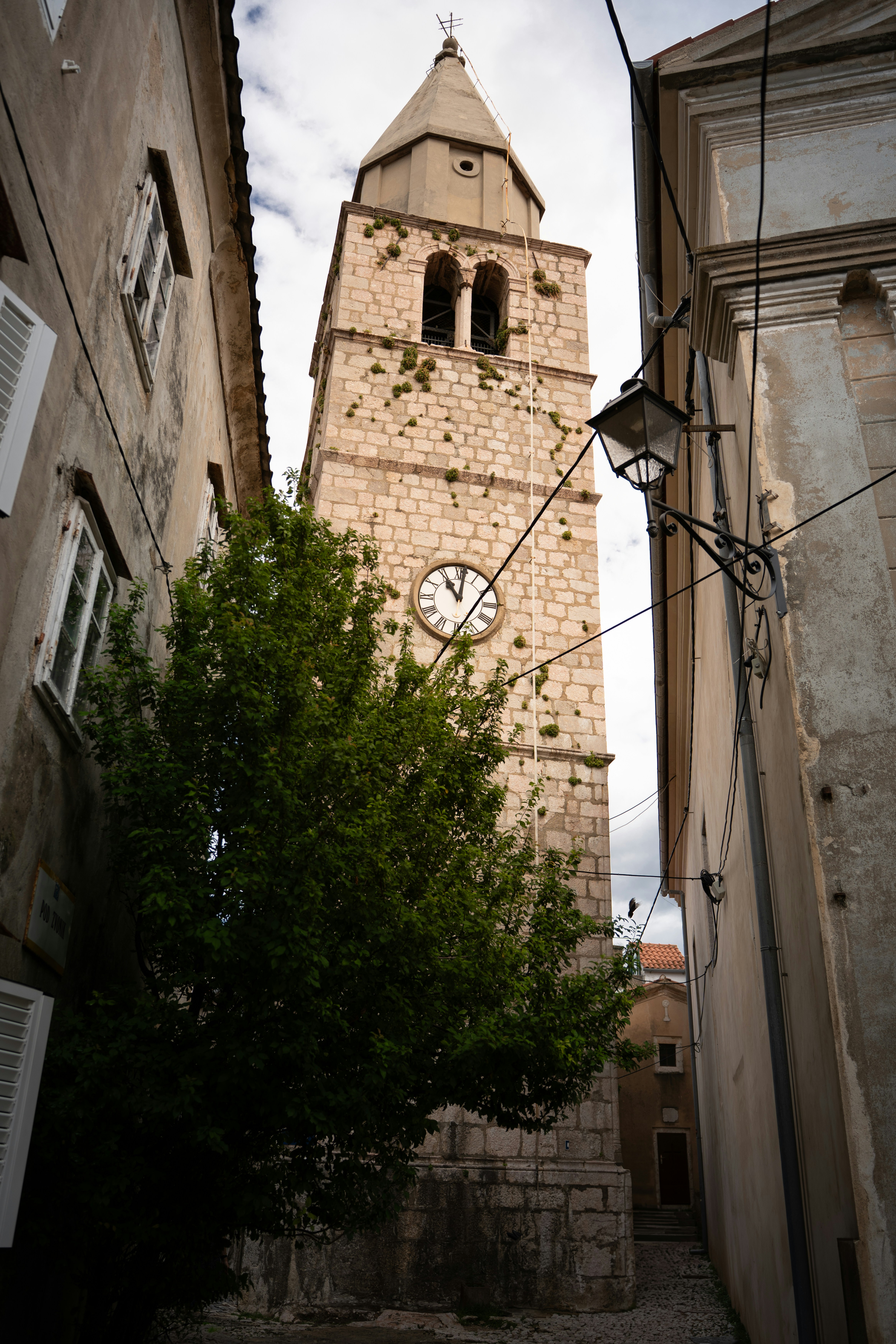 Stone church tower with clock in narrow alleyway