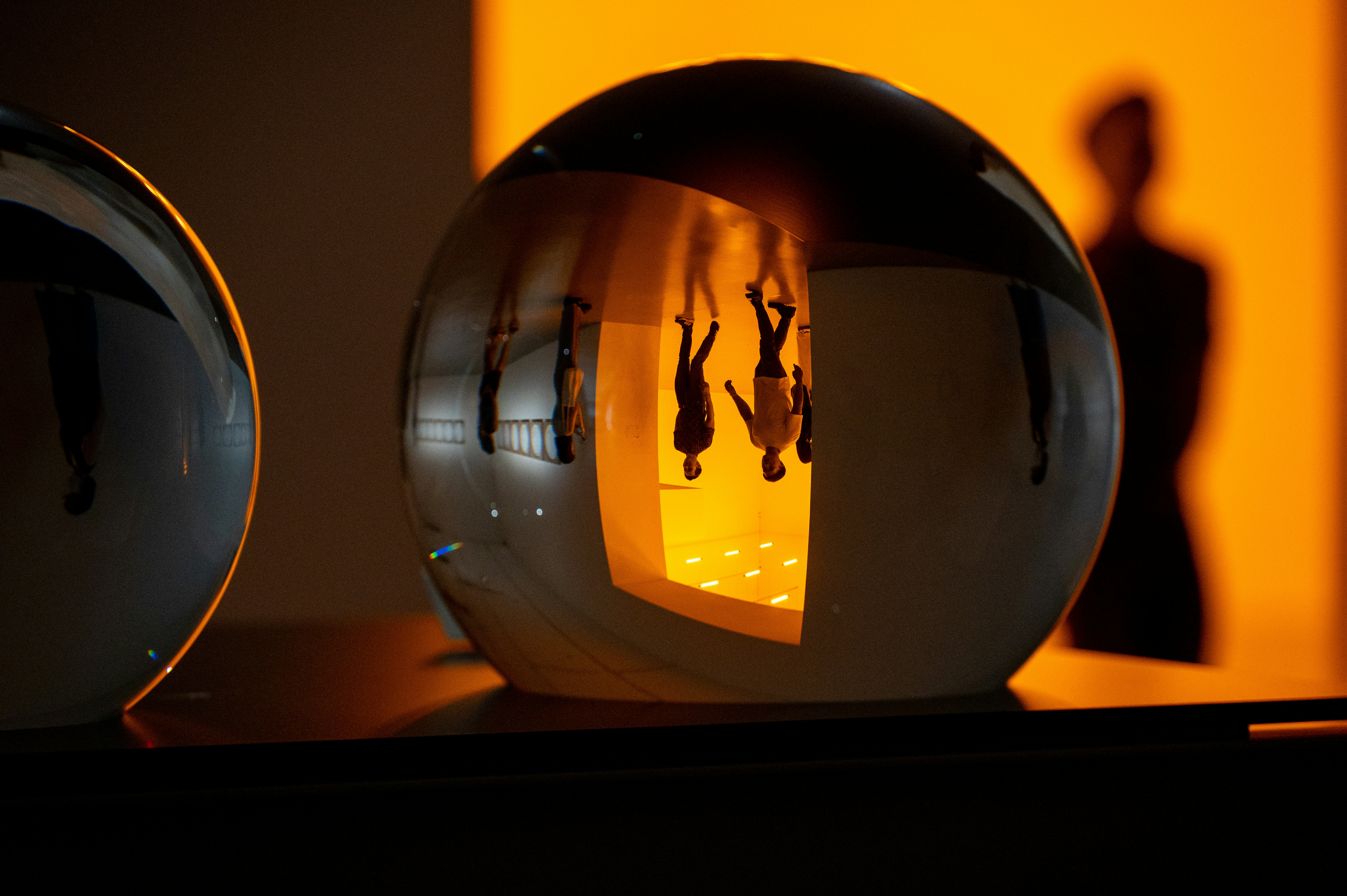 Reflective spheres capturing silhouettes against a vibrant orange backdrop, creating an intriguing interplay of light and form.
