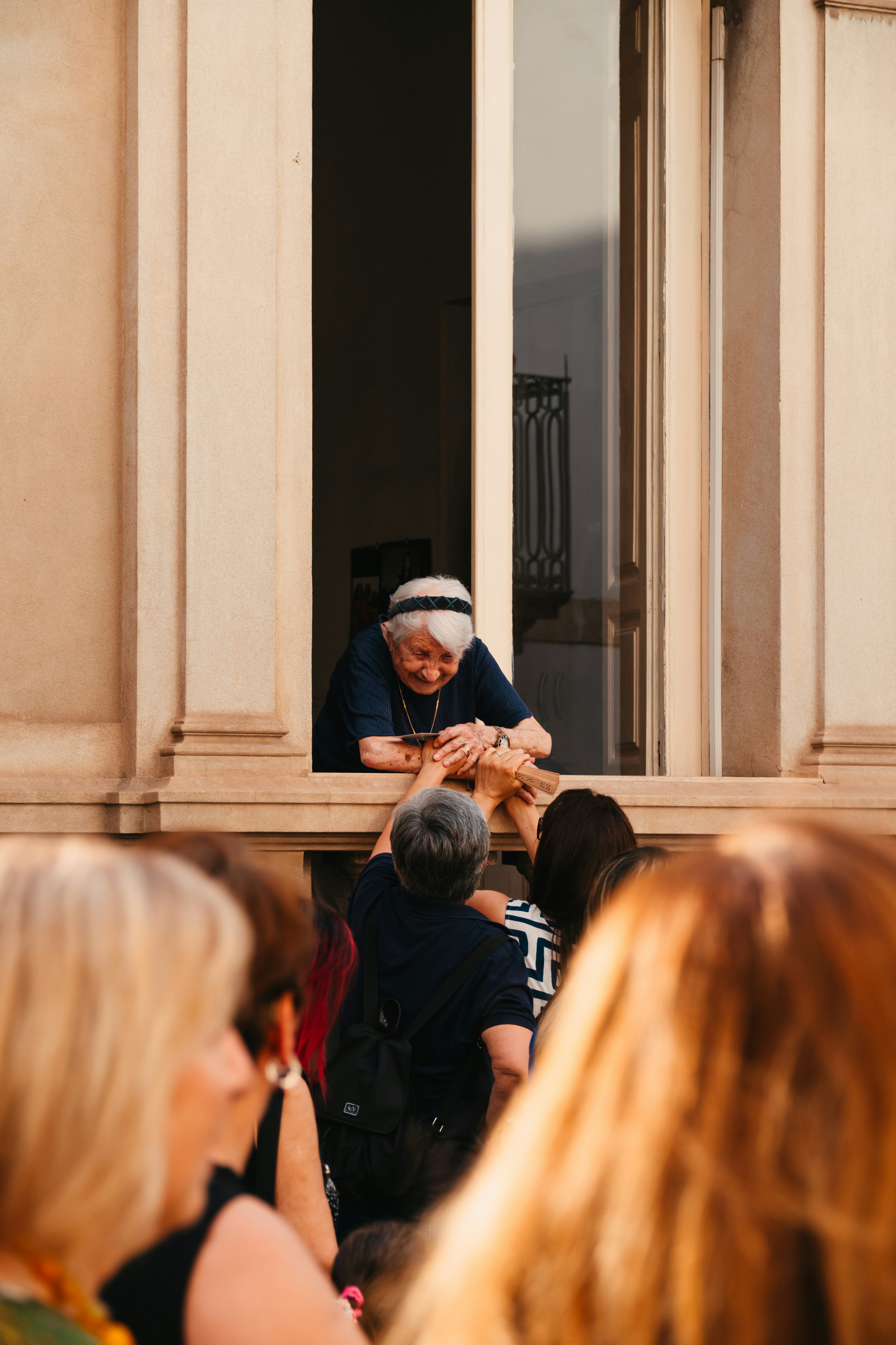 Elderly woman interacting with a crowd from a window, showcasing a moment of connection and community spirit.
