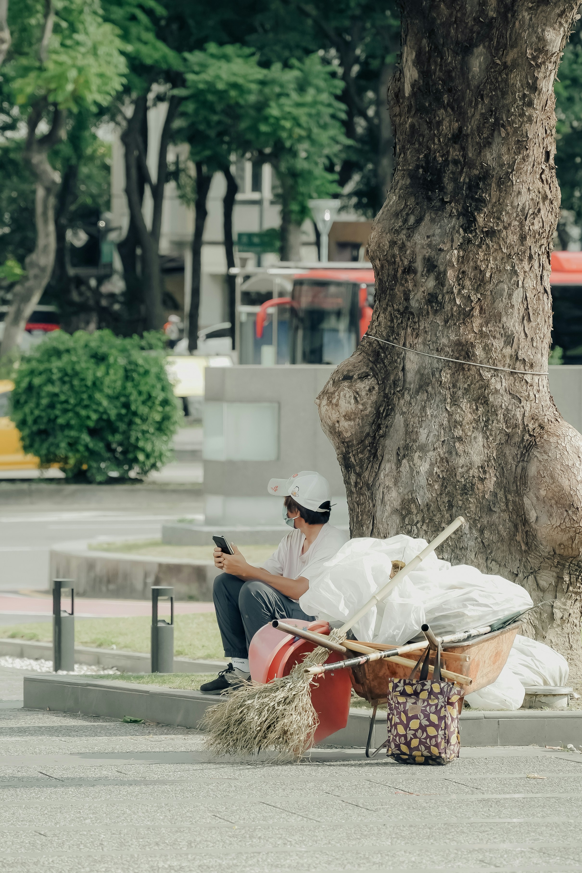 Person with cleaning supplies sits by tree