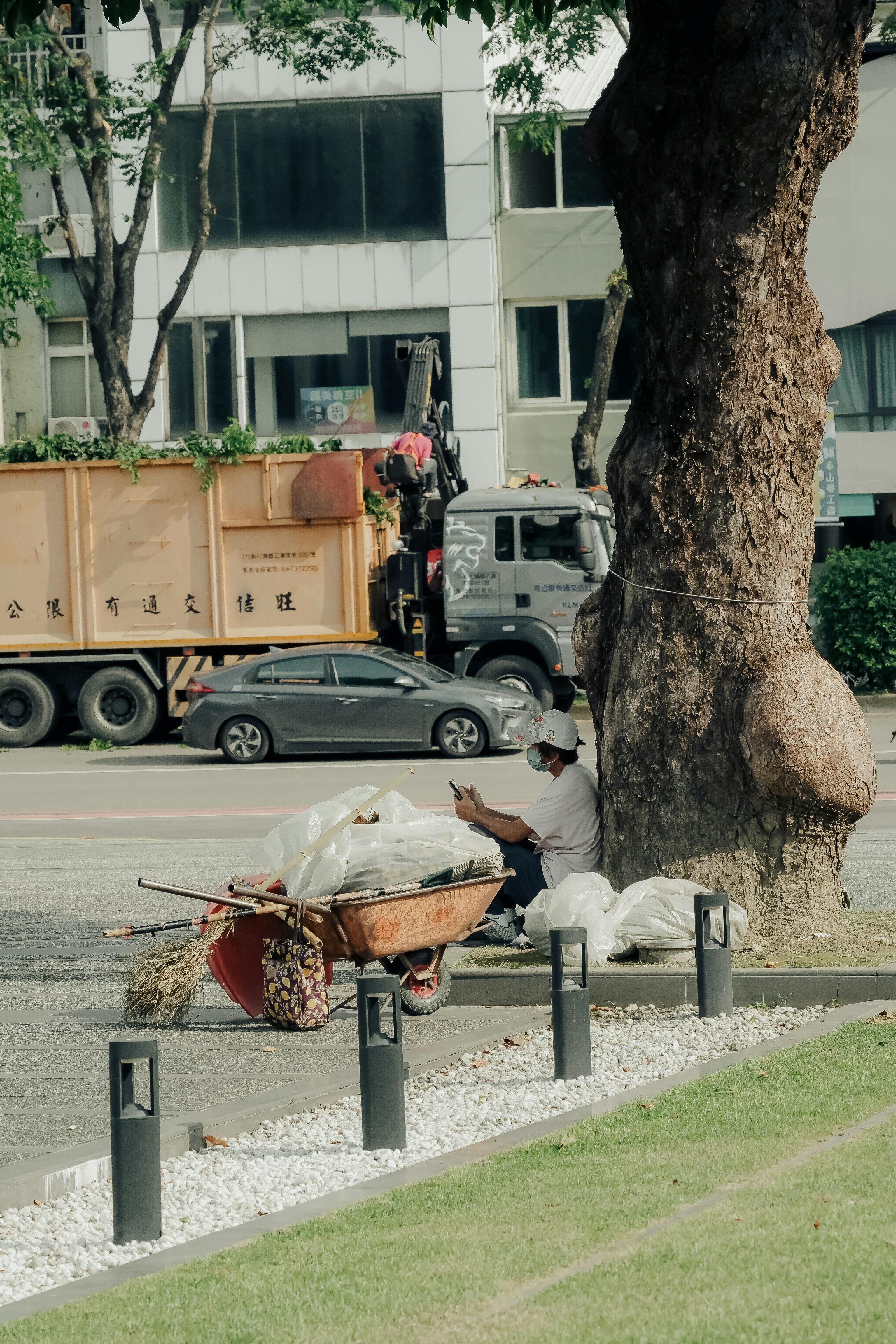 Man rests by tree next to cleanup cart and truck
