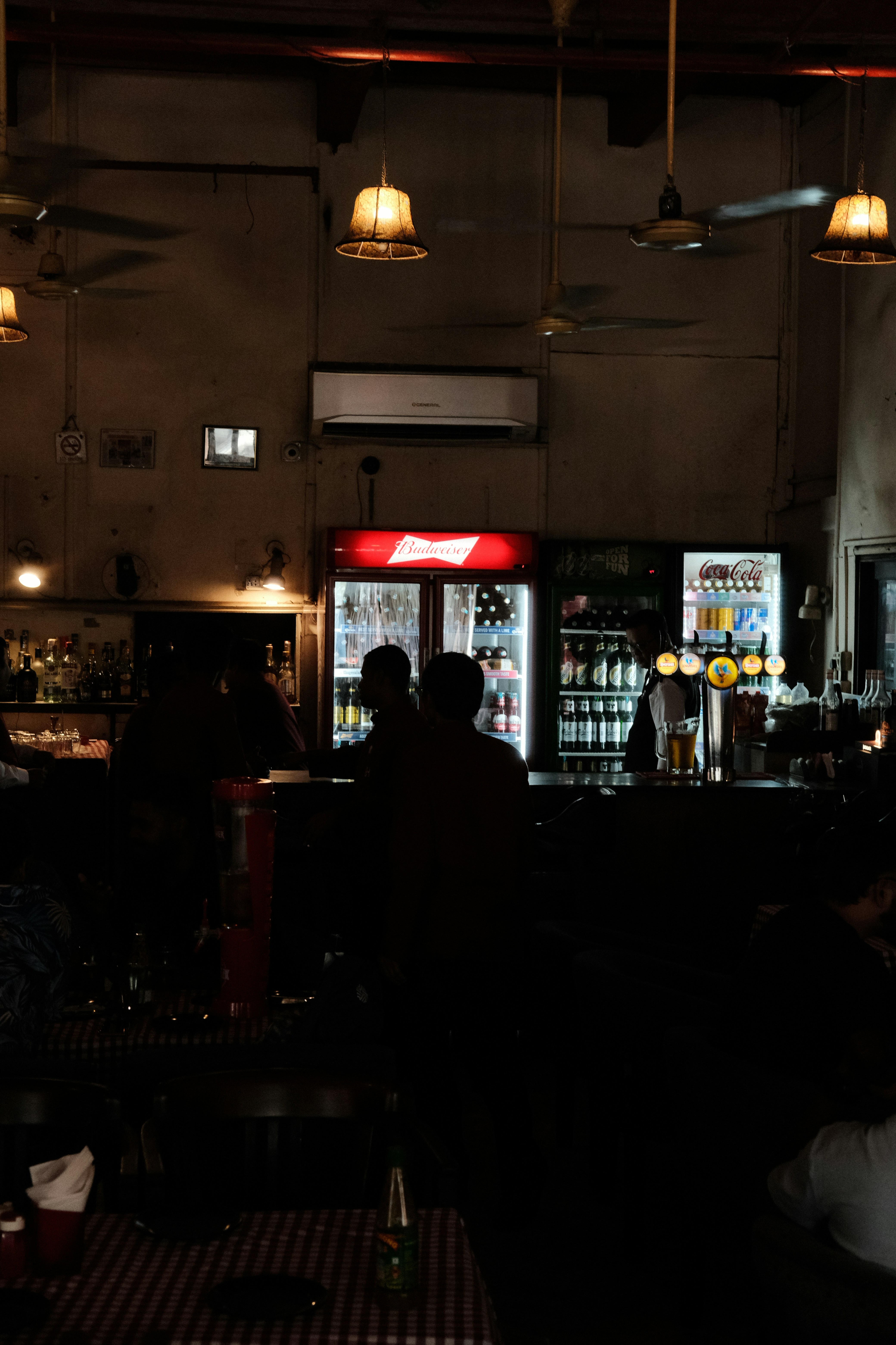 People at a dimly lit bar with refrigerators full beverage coolers.