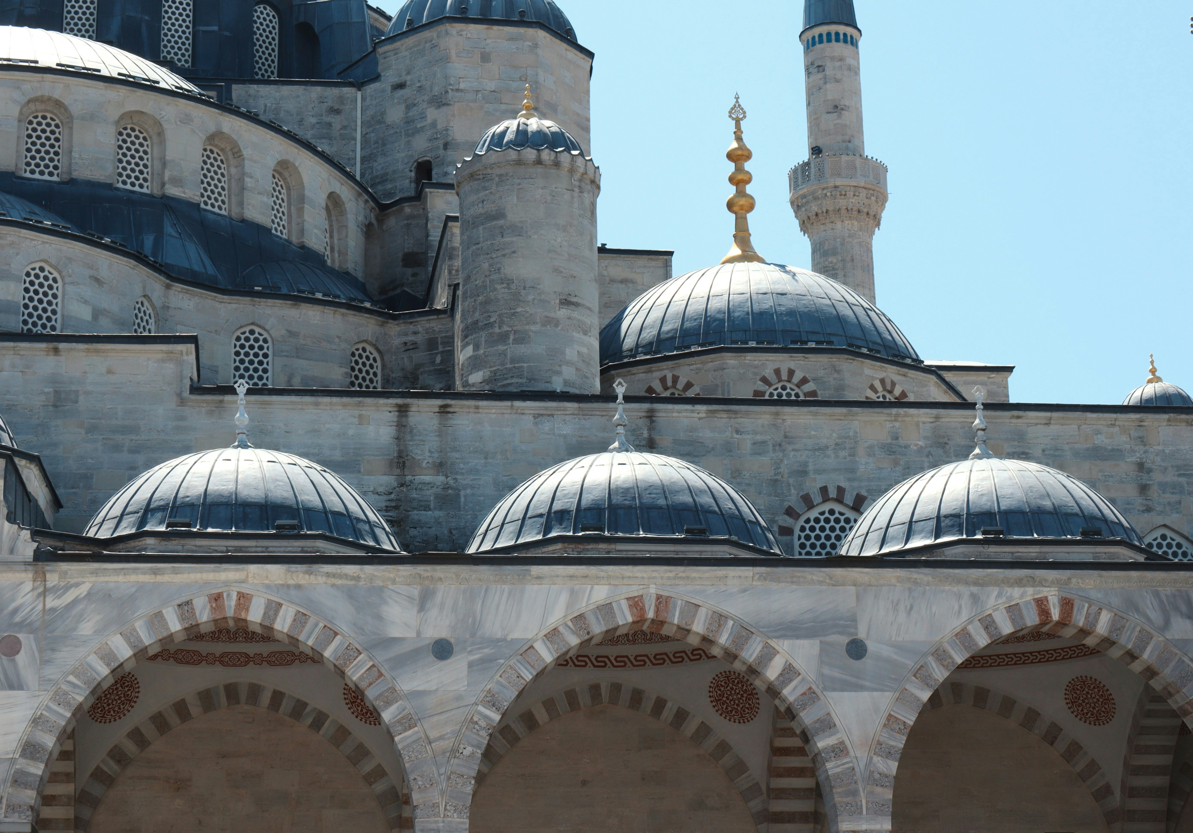 Intricate domes and arches of a historic mosque under a clear blue sky. The design showcases a blend of artistry and engineering.