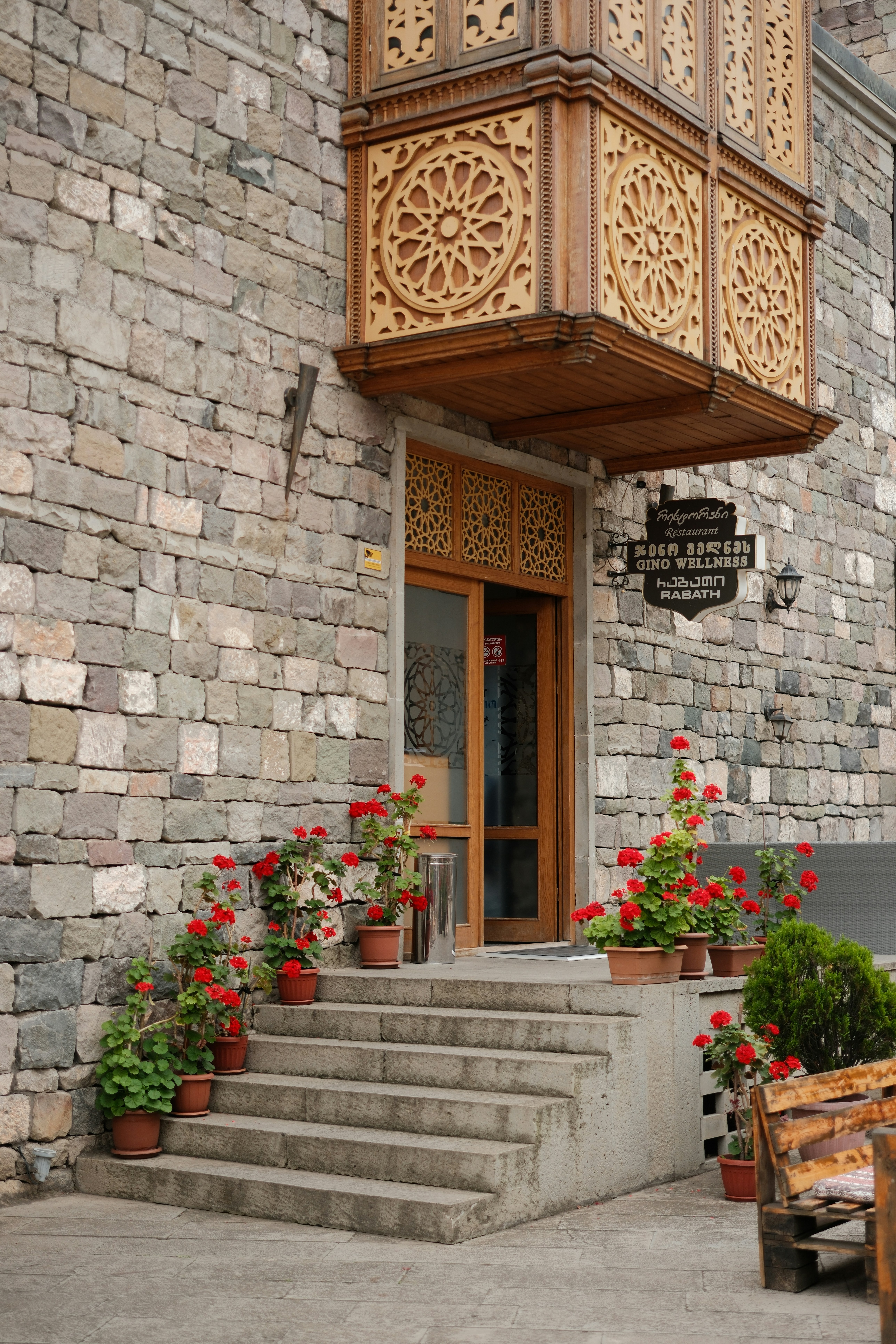 Stone building entrance with ornate wooden balcony and flowers