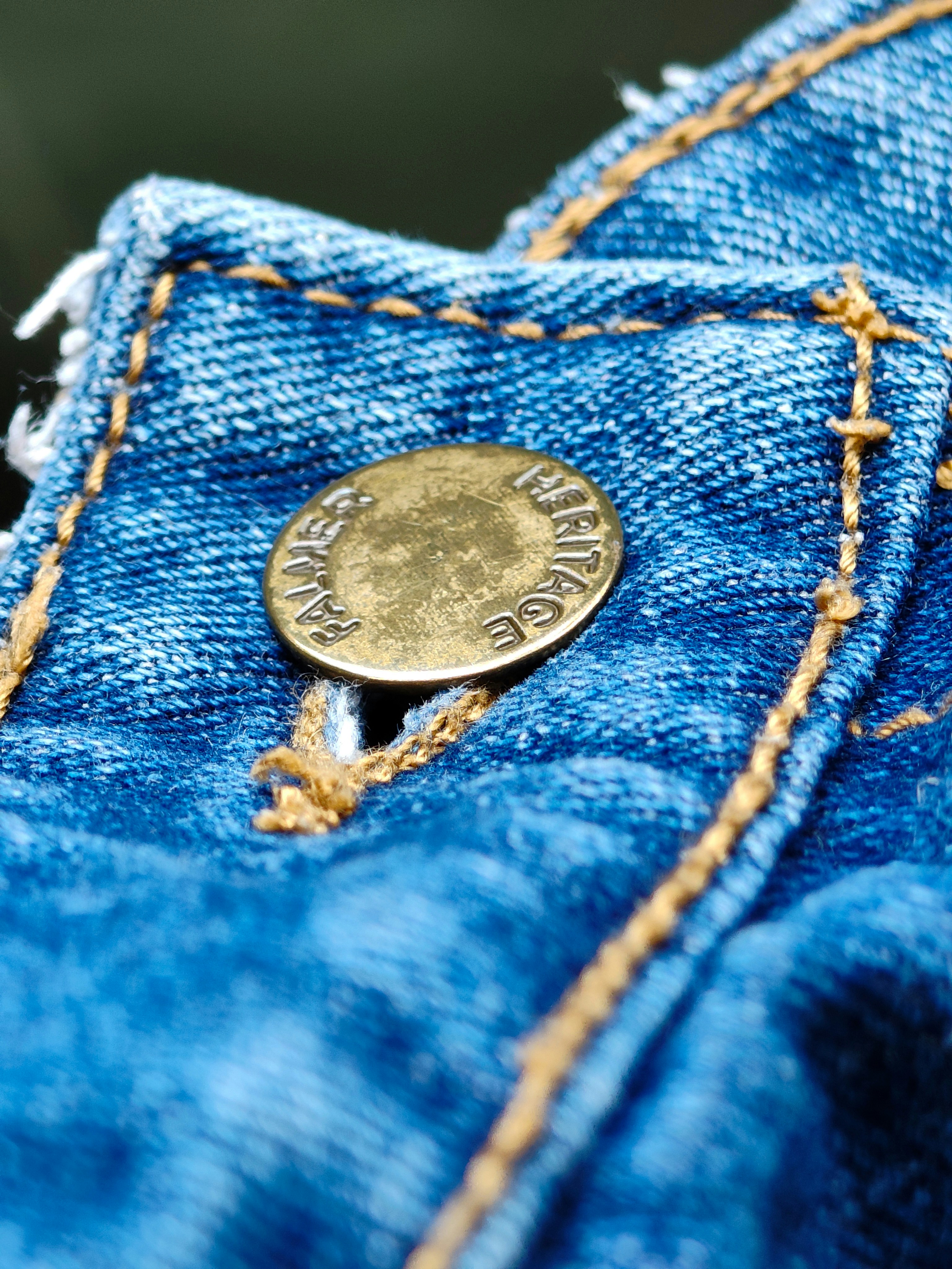 Close-up of a brass button on blue denim jeans.