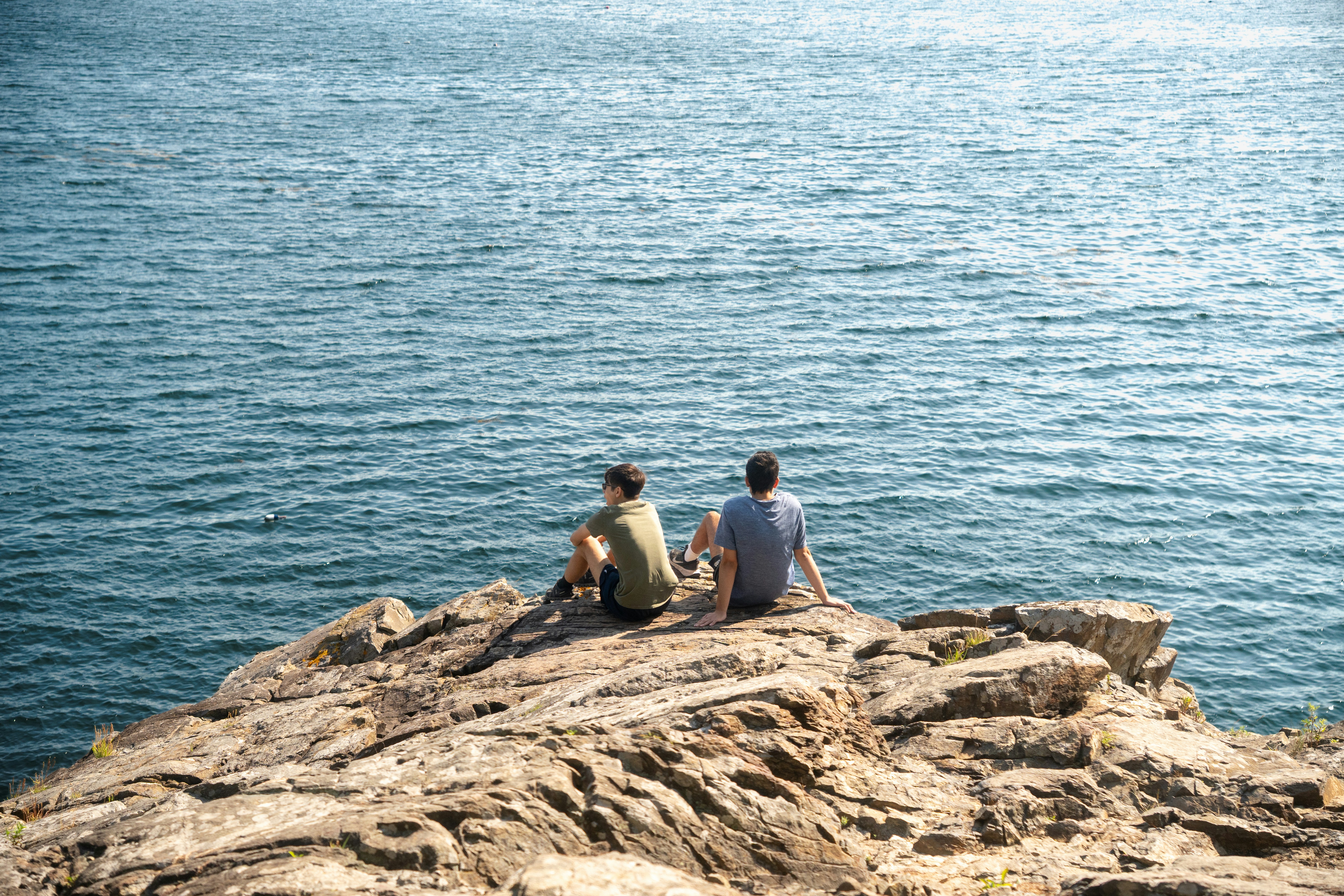 Two individuals seated on a rocky outcrop, gazing over the tranquil water, enjoying a moment of serenity.