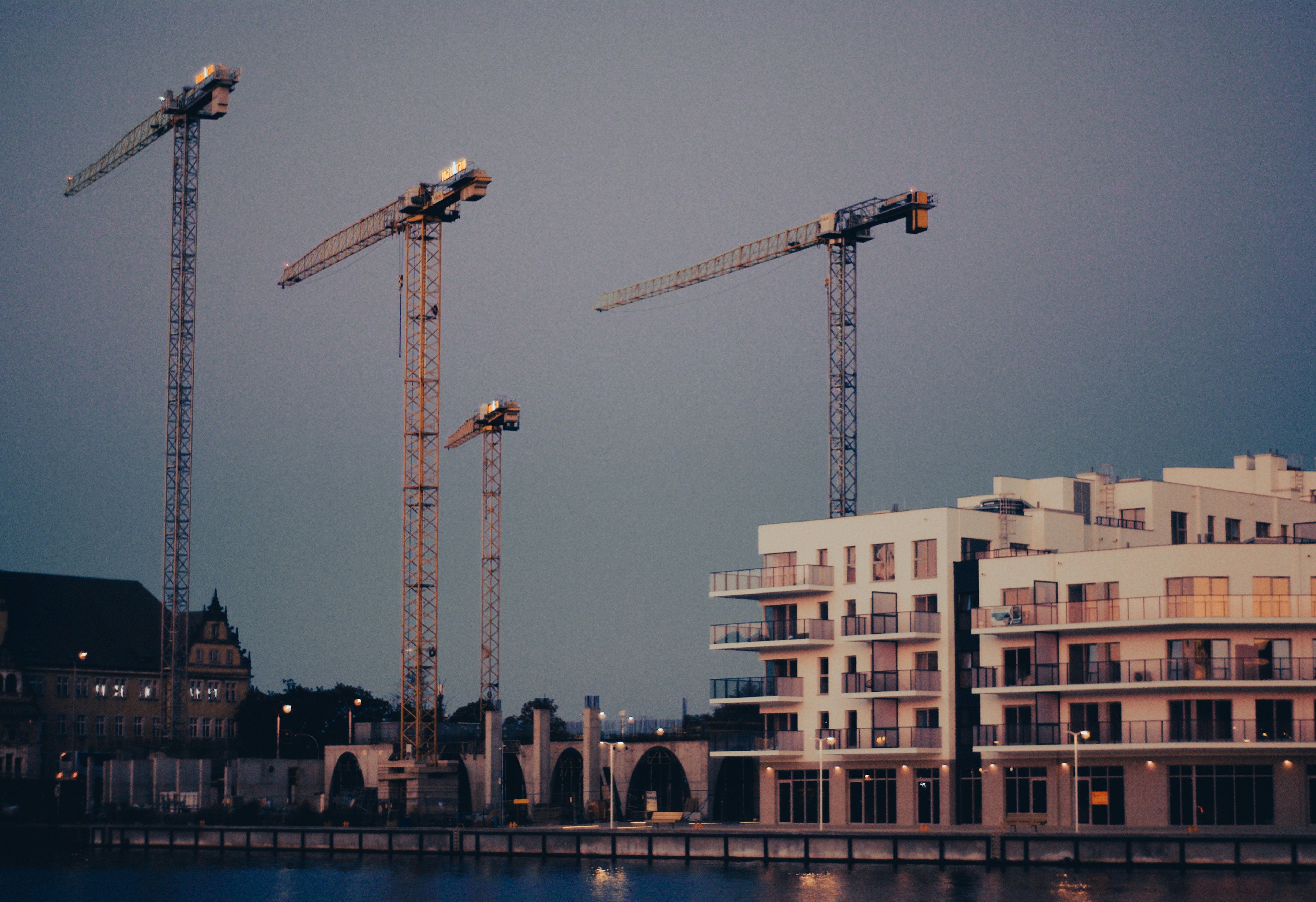 Construction cranes near modern buildings by water