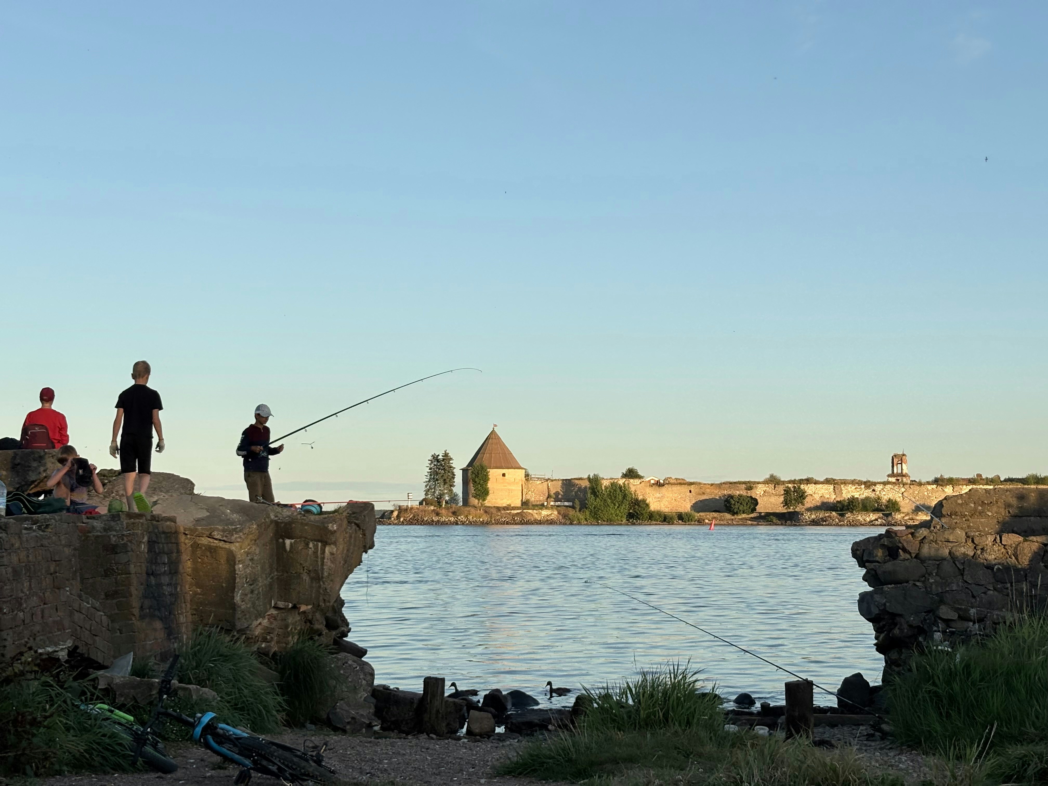 People fishing on a sunny day near a historic building.