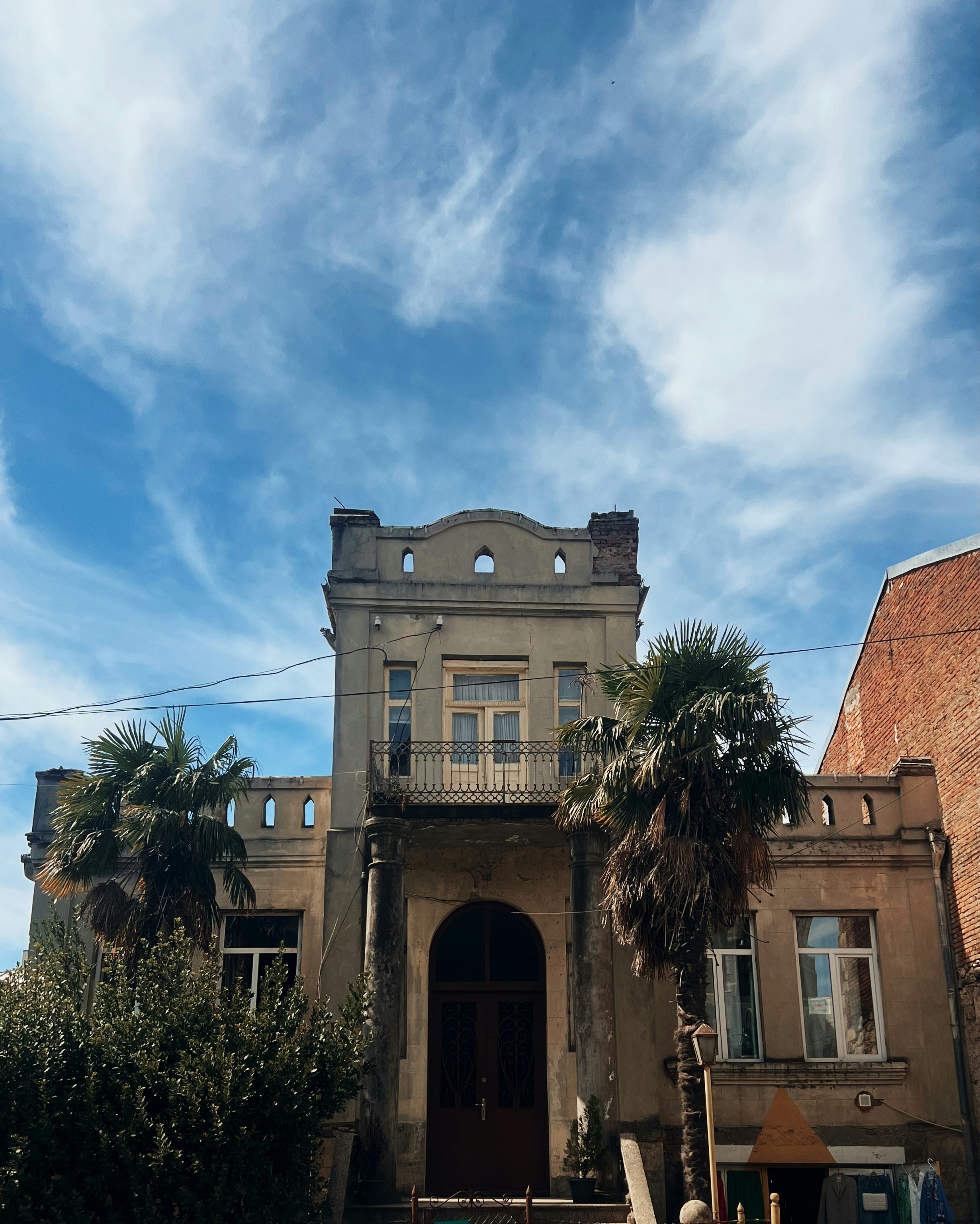 An old building featuring unique architectural details, framed by lush palm trees and a vibrant blue sky. The structure hints at a rich history and cultural significance.