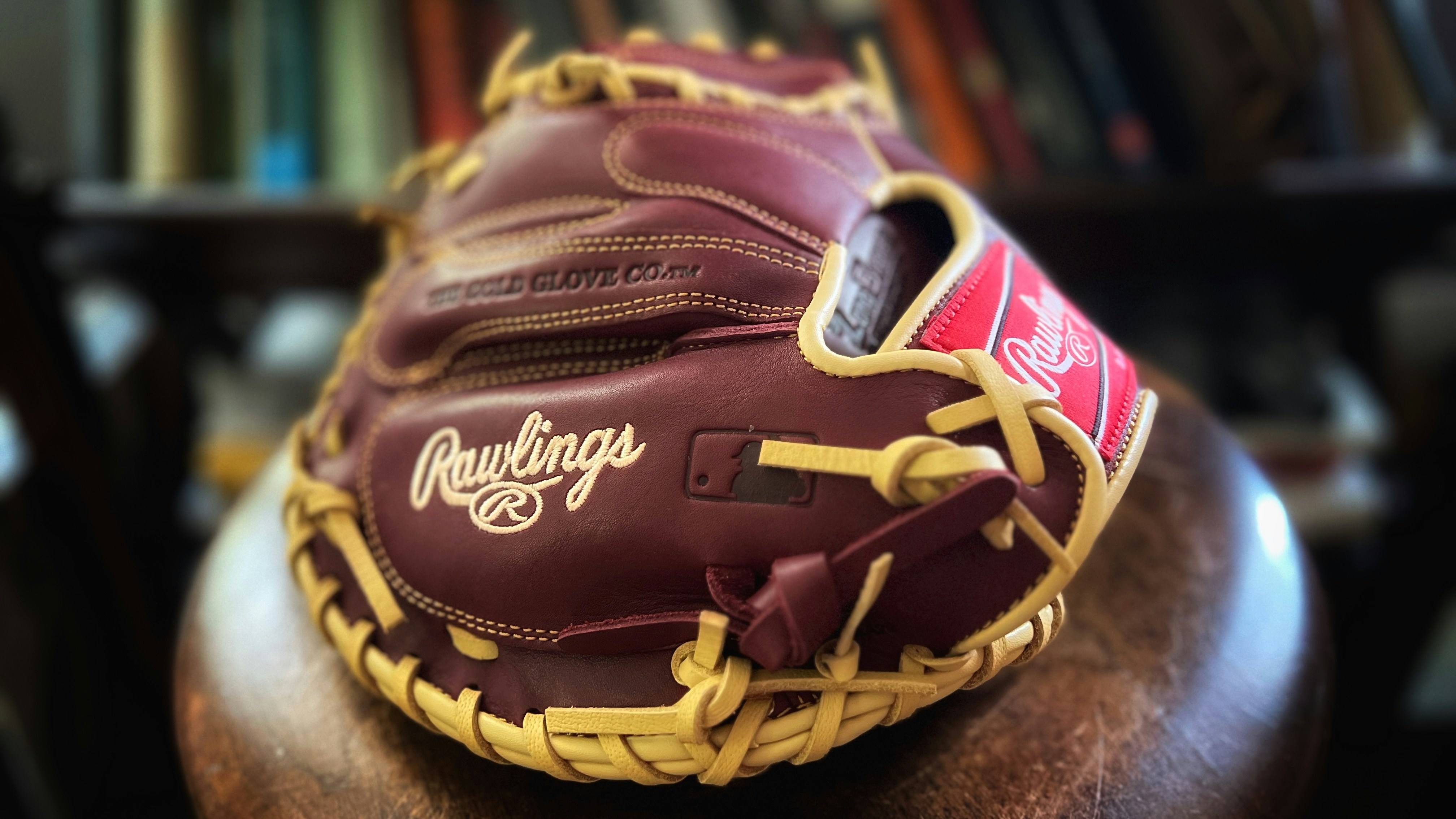 A close-up of a Rawlings baseball glove resting on a wooden surface, showcasing its craftsmanship and rich color details.