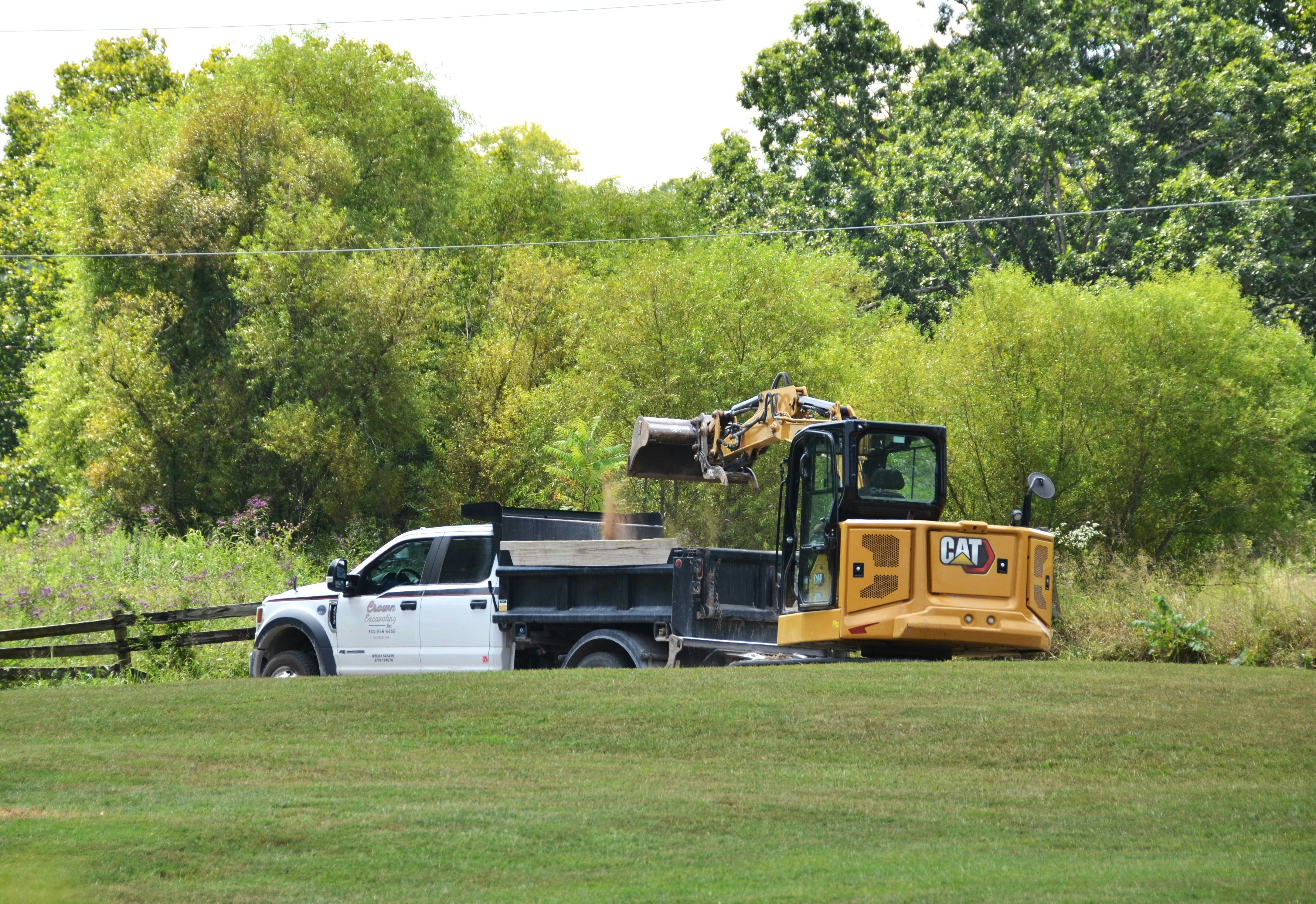Construction Tug of War: CAT Excavator and White Service Truck on a Green Crest
