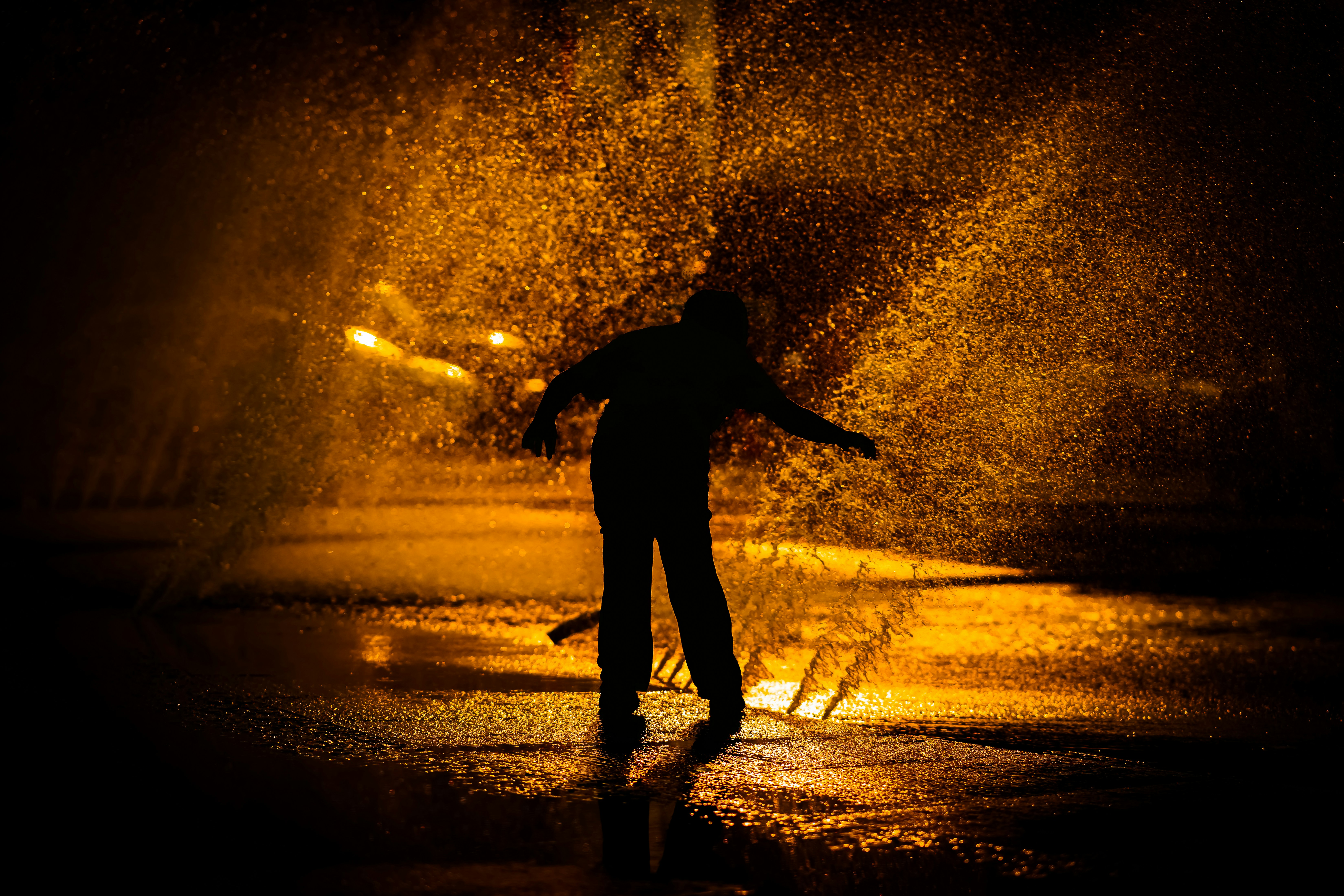 Silhouette of a person joyfully interacting with splashes of water against a backdrop of warm, glowing lights.