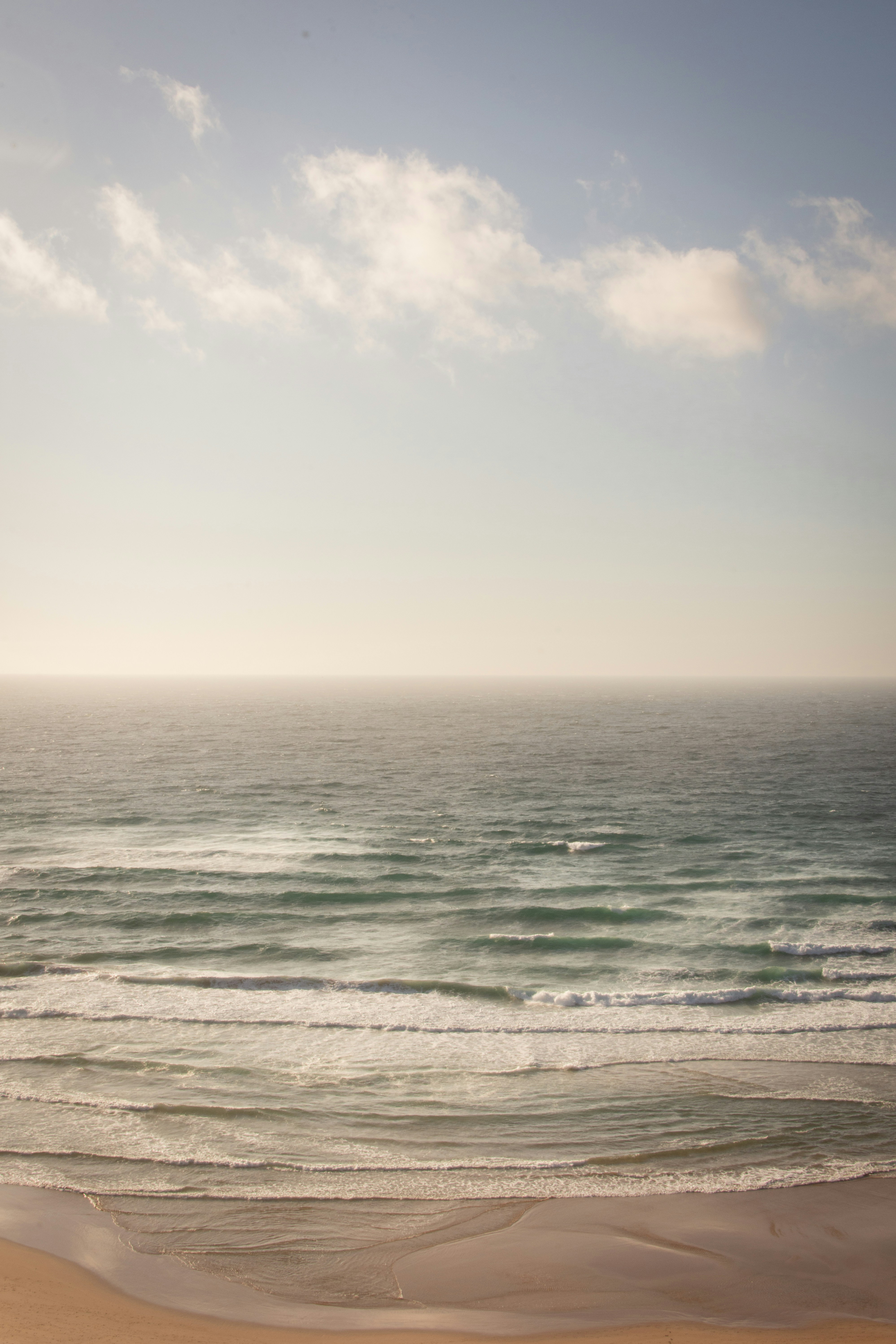 Gentle waves caress the sandy shore under a soft, pastel sky. The tranquil scene captures the essence of a serene coastal landscape.