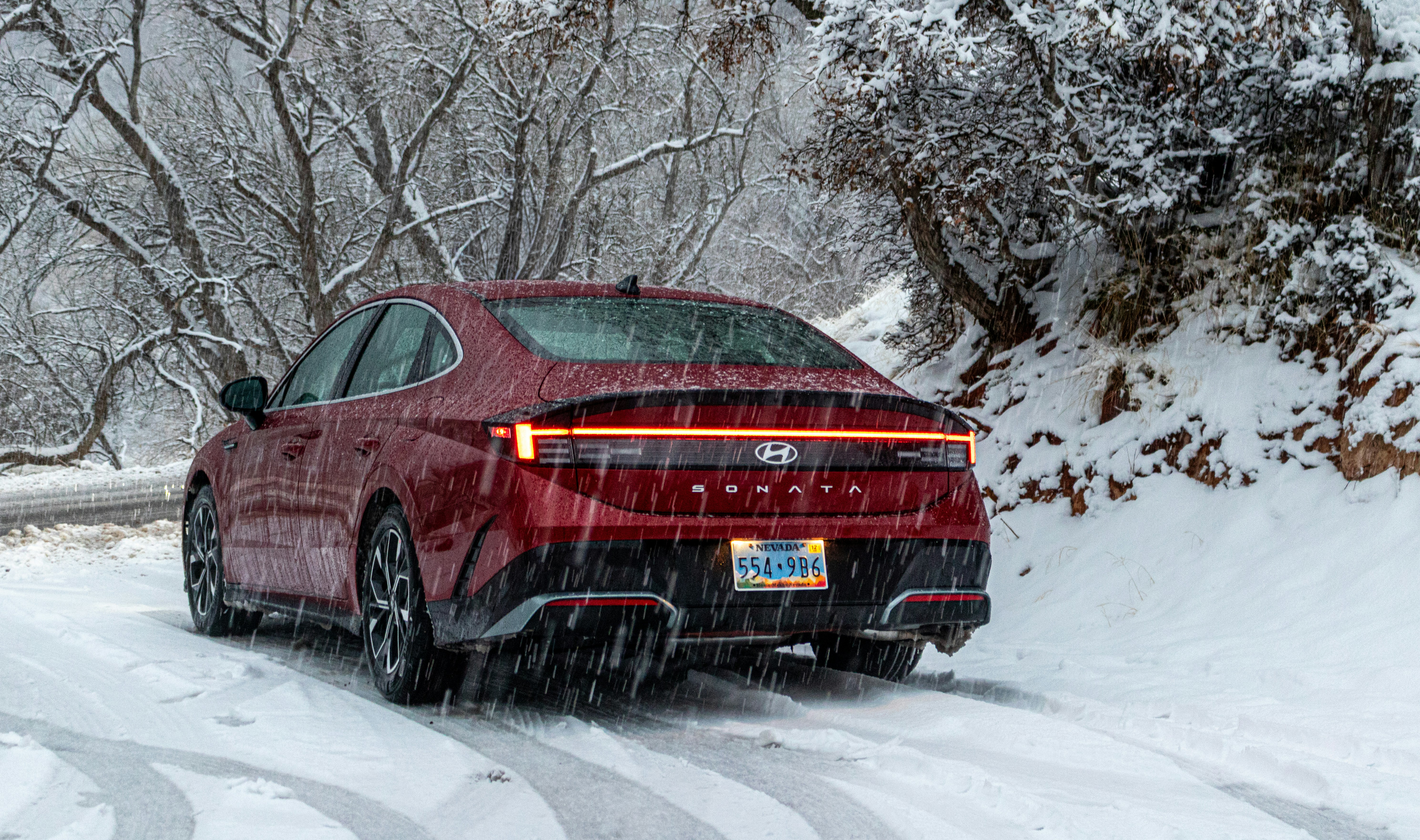A red Hyundai Sonata parked in the midst of a snowstorm at Zion National Park, Utah. The car’s bold color stands out against the muted whites and grays of a cold winter day, creating a striking visual contrast. | Red car driving on a snowy road