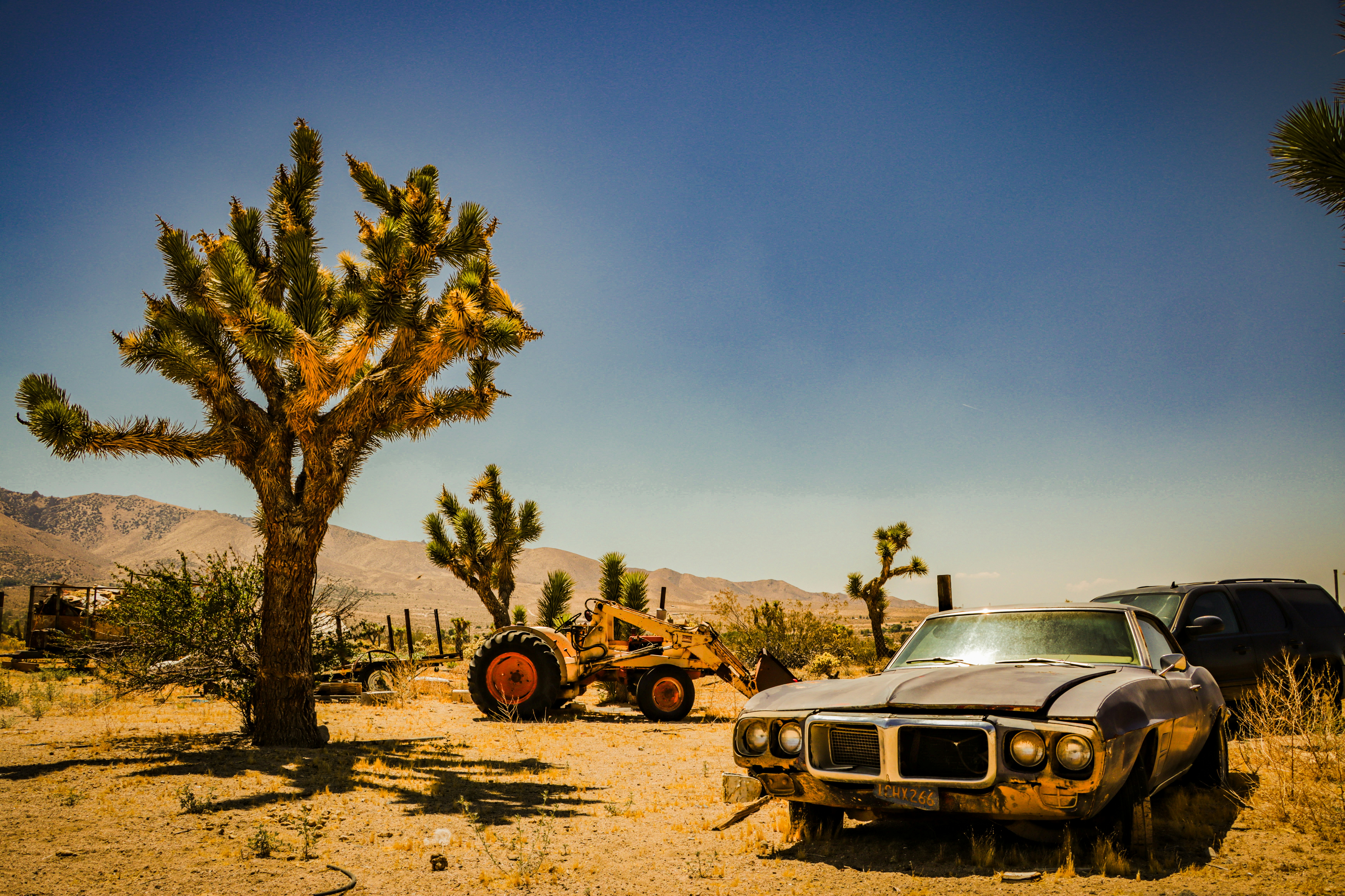 Abandoned car and tractor in a desert landscape.