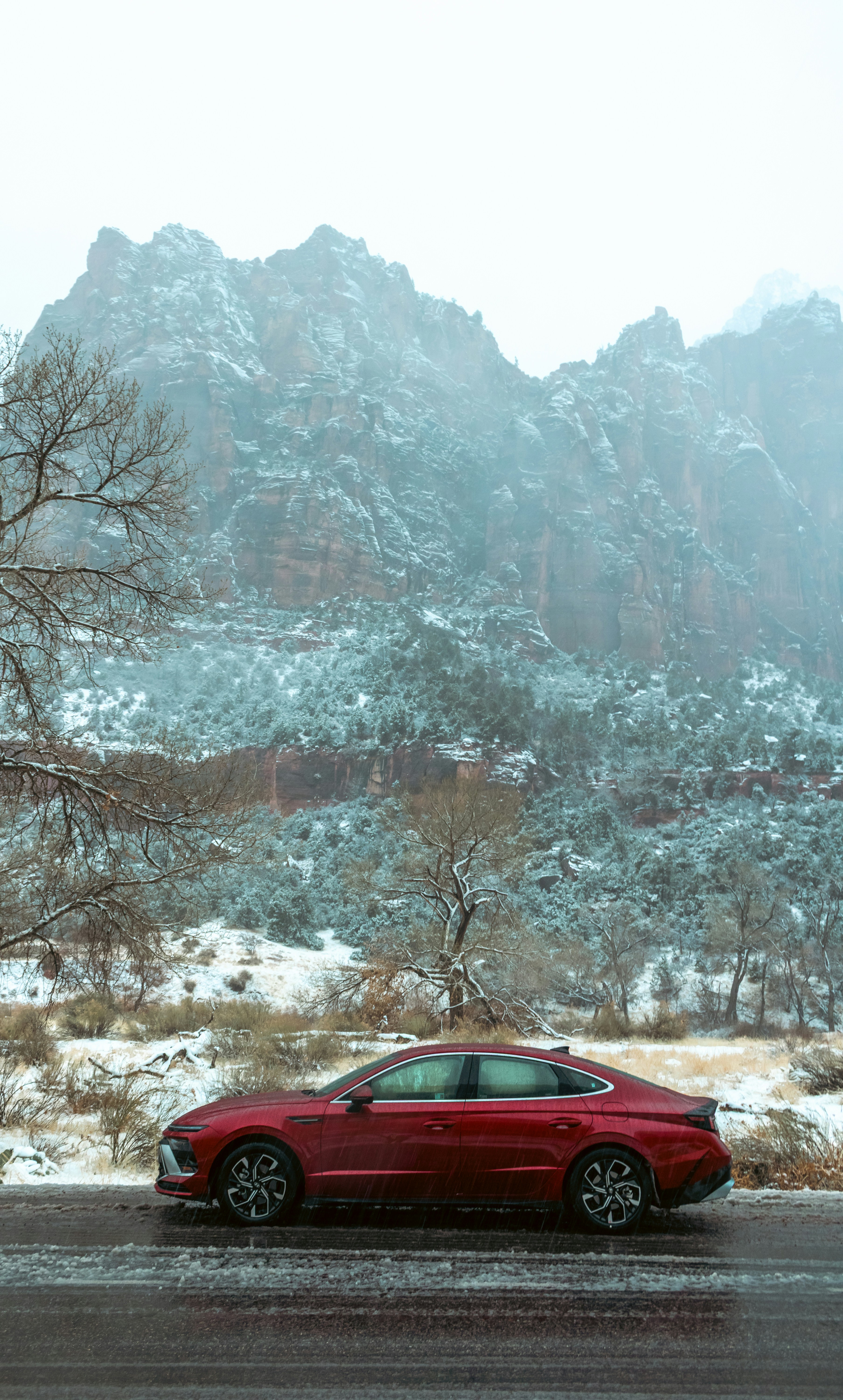 Crimson Sedan on a Snow-Dusted Highway Beneath Rugged Canyon Peaks