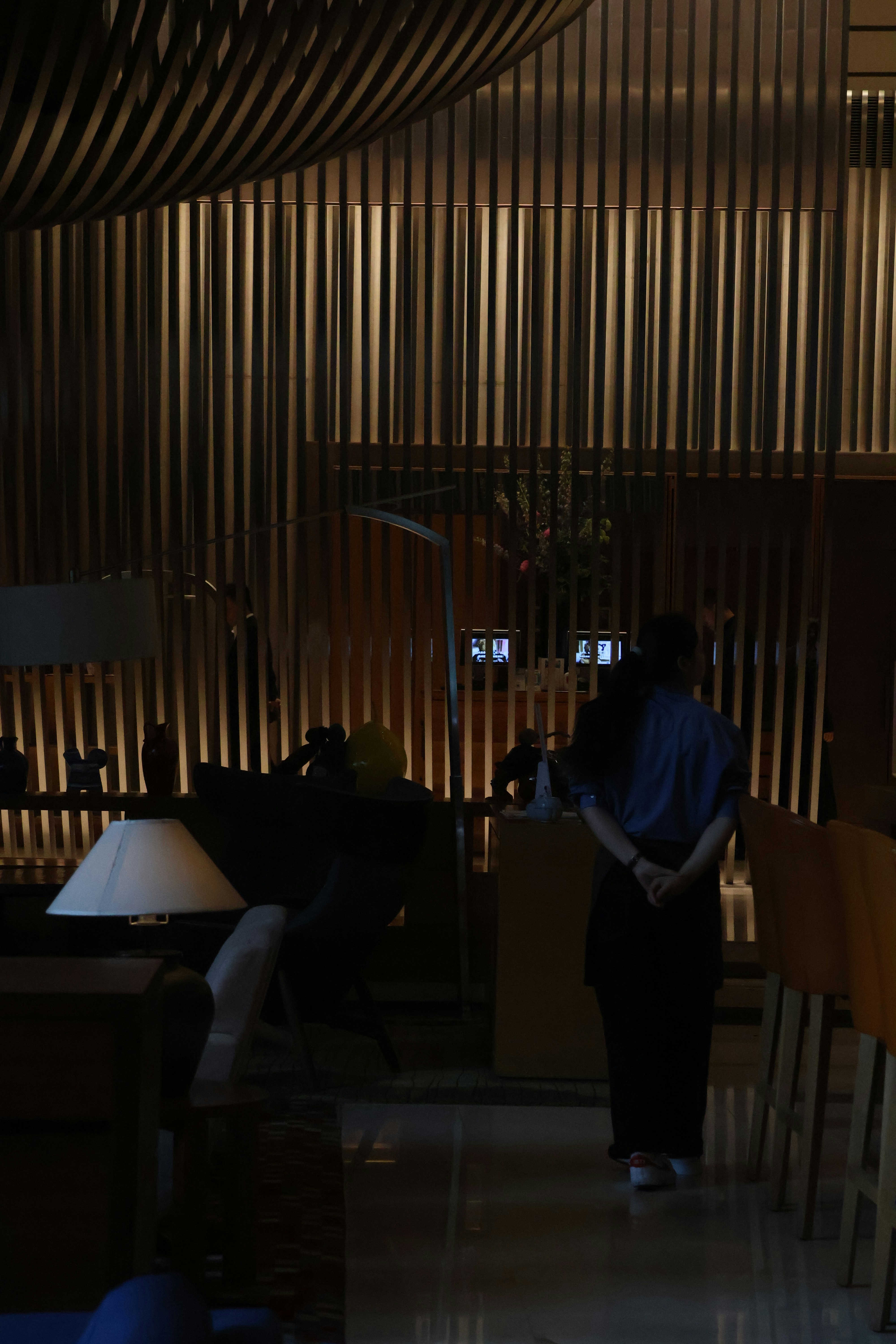Person standing in a dimly lit lobby with wooden accents