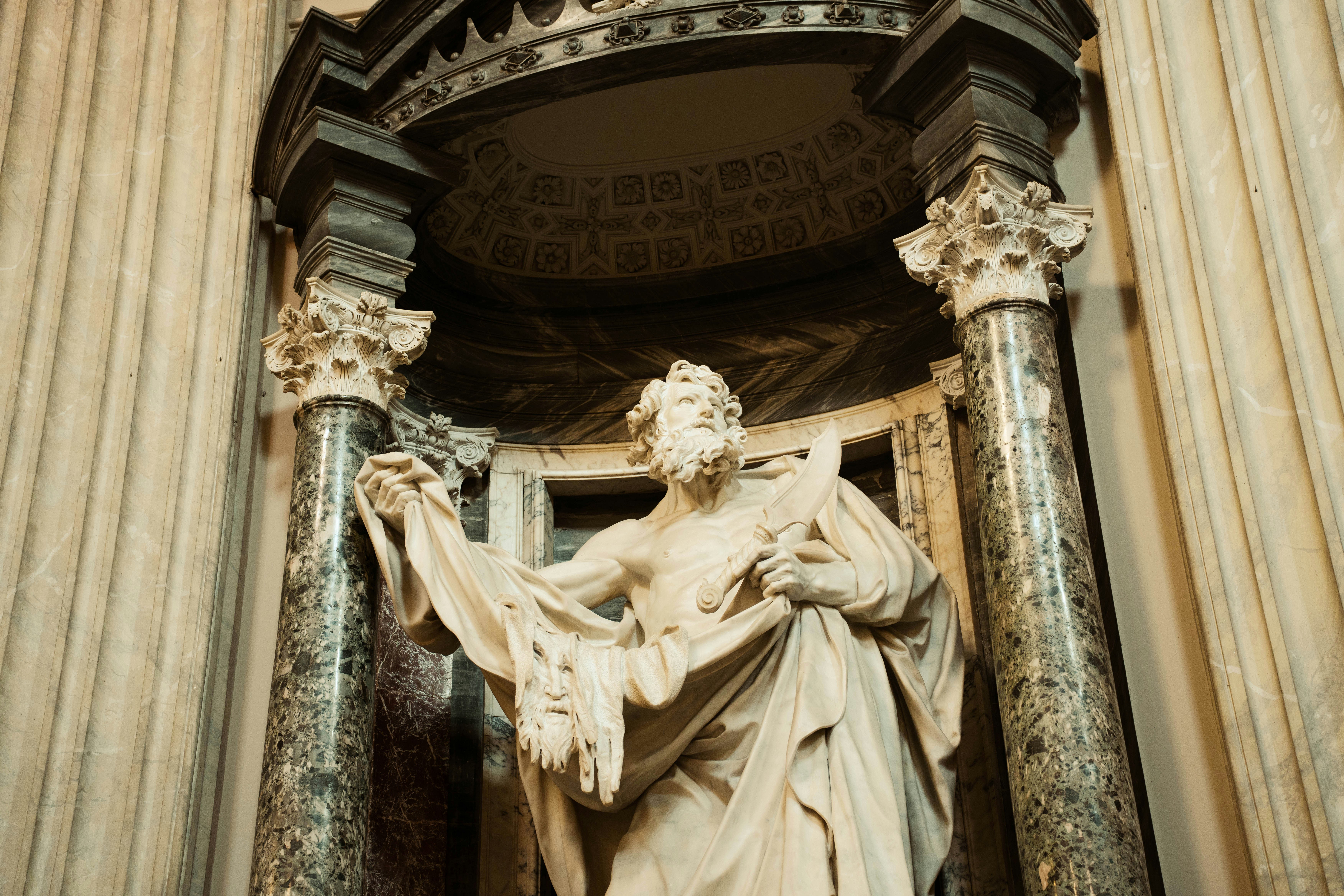 Intricate marble statue of a figure draped in flowing garments, set against a backdrop of ornate columns and a detailed ceiling. The scene conveys a sense of grandeur and artistry.