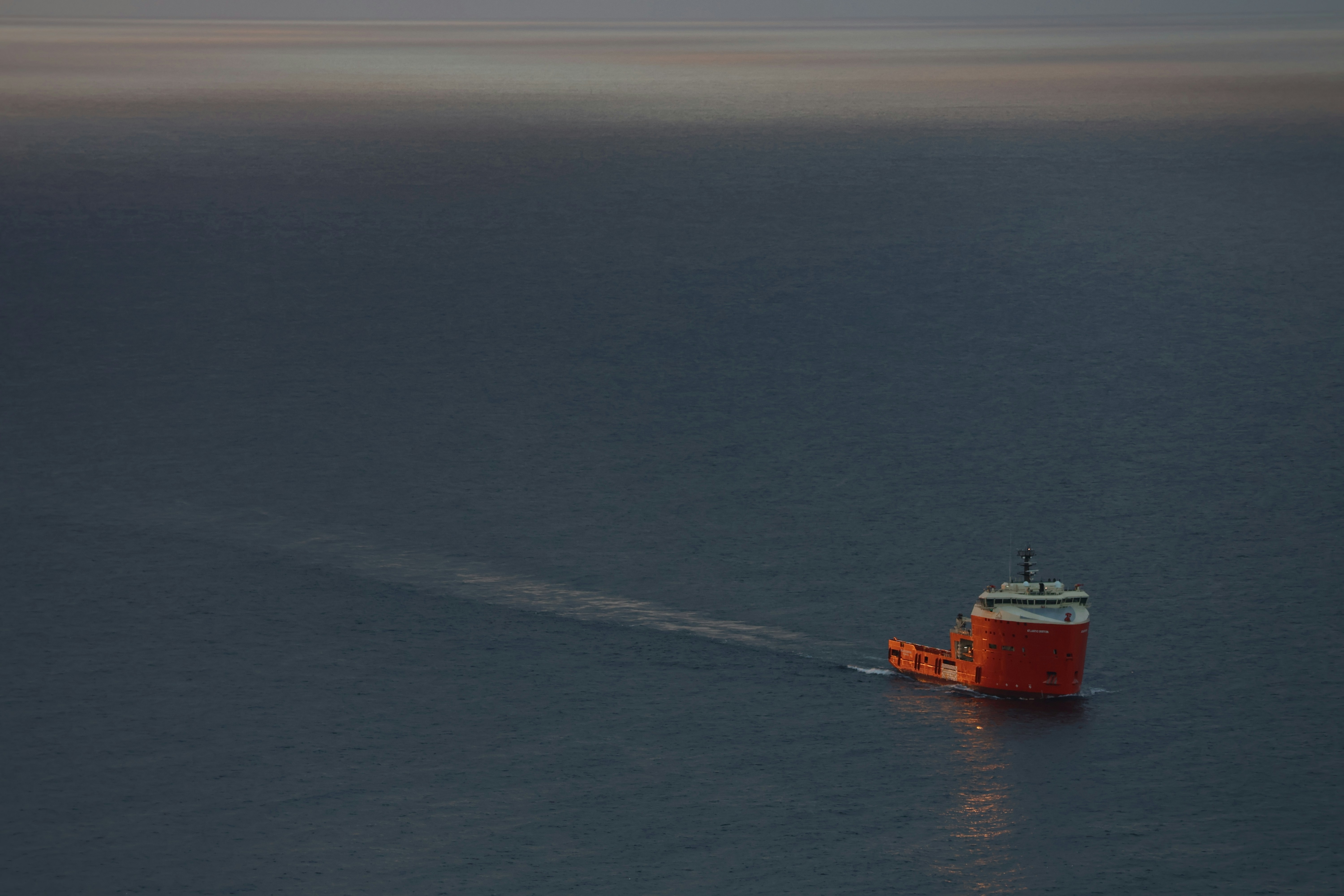 Orange vessel sailing on dark ocean at dusk