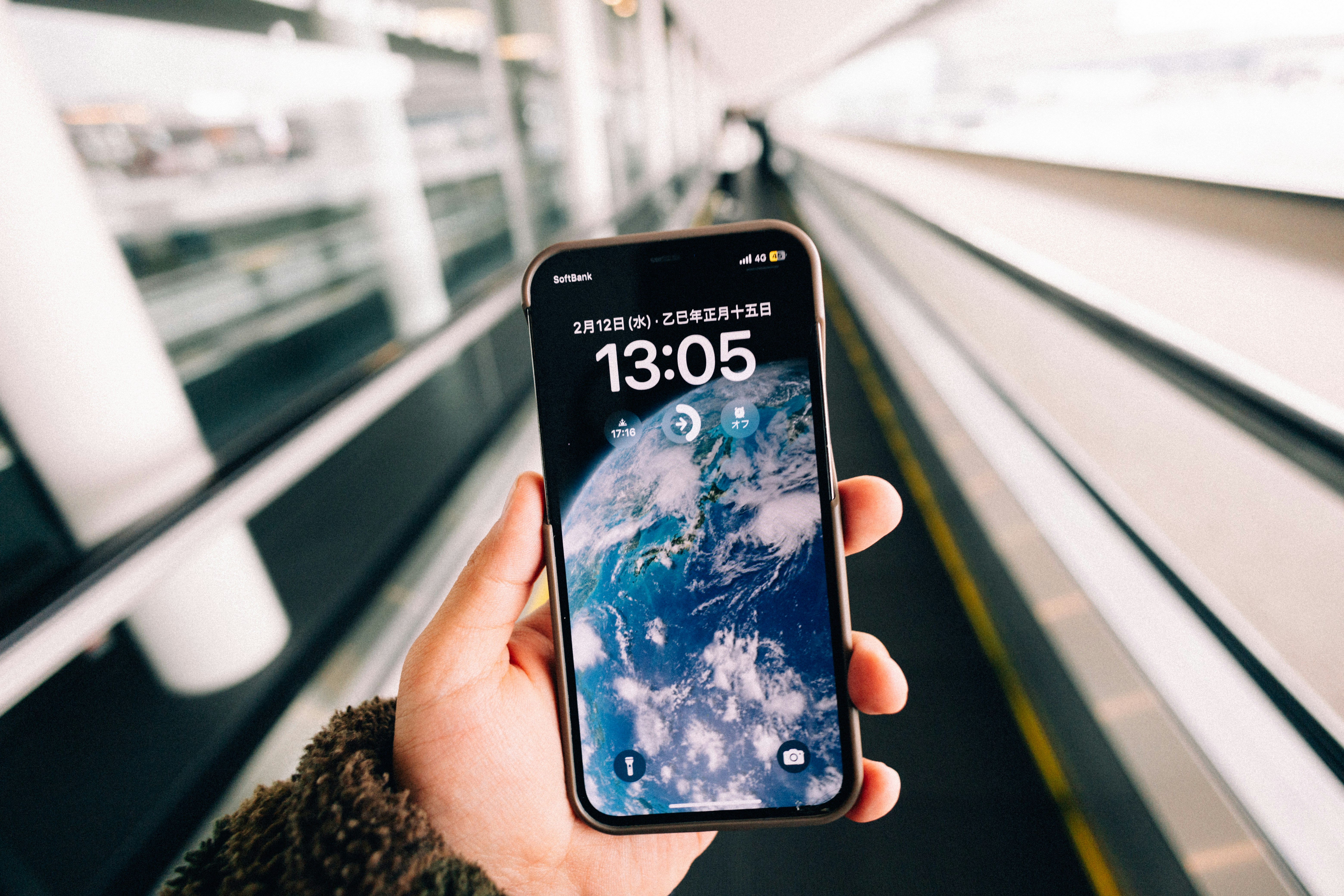 Person holding smartphone with earth wallpaper on escalator.