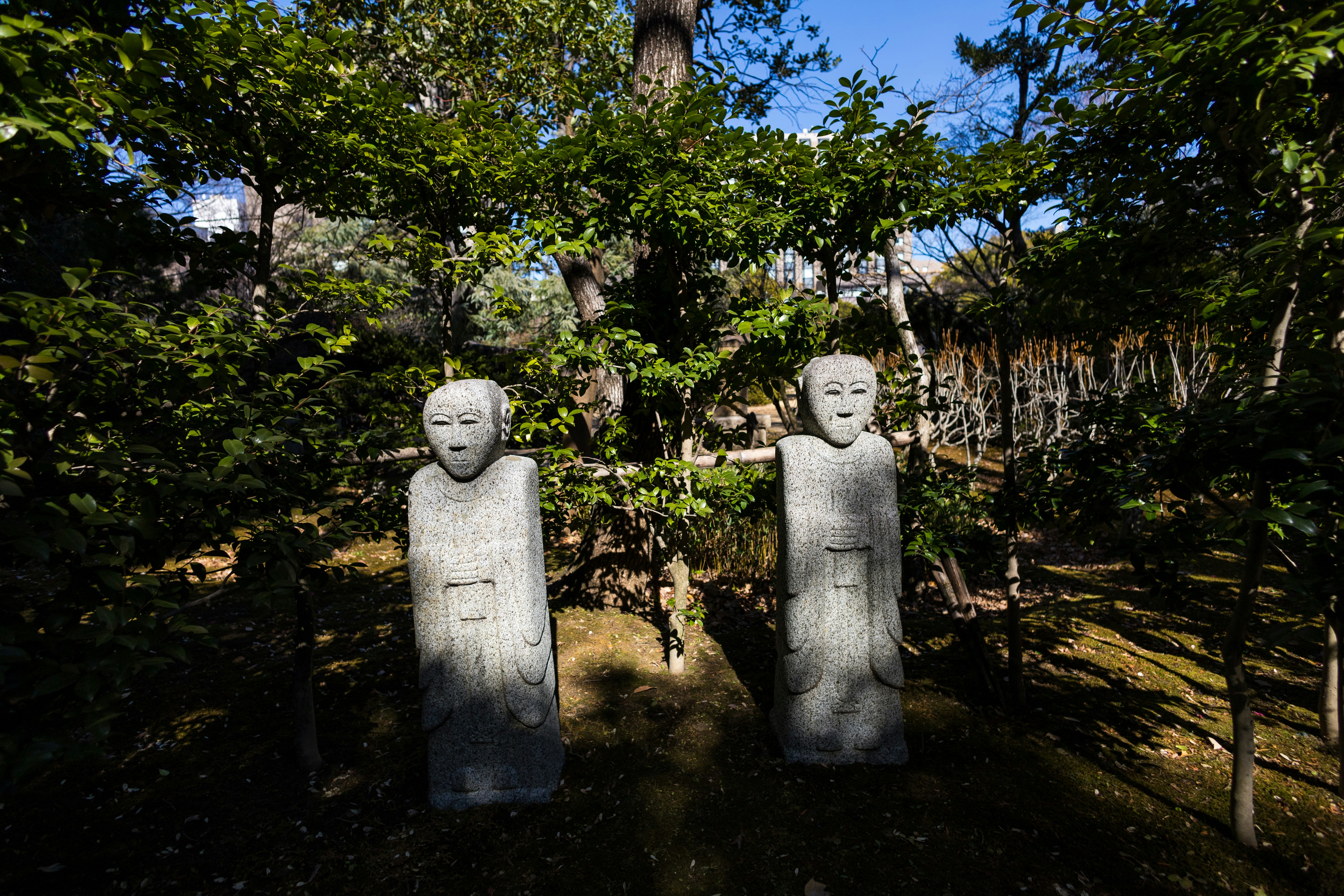 Two stone statues stand among trees in a garden. photo – Free Woman ...