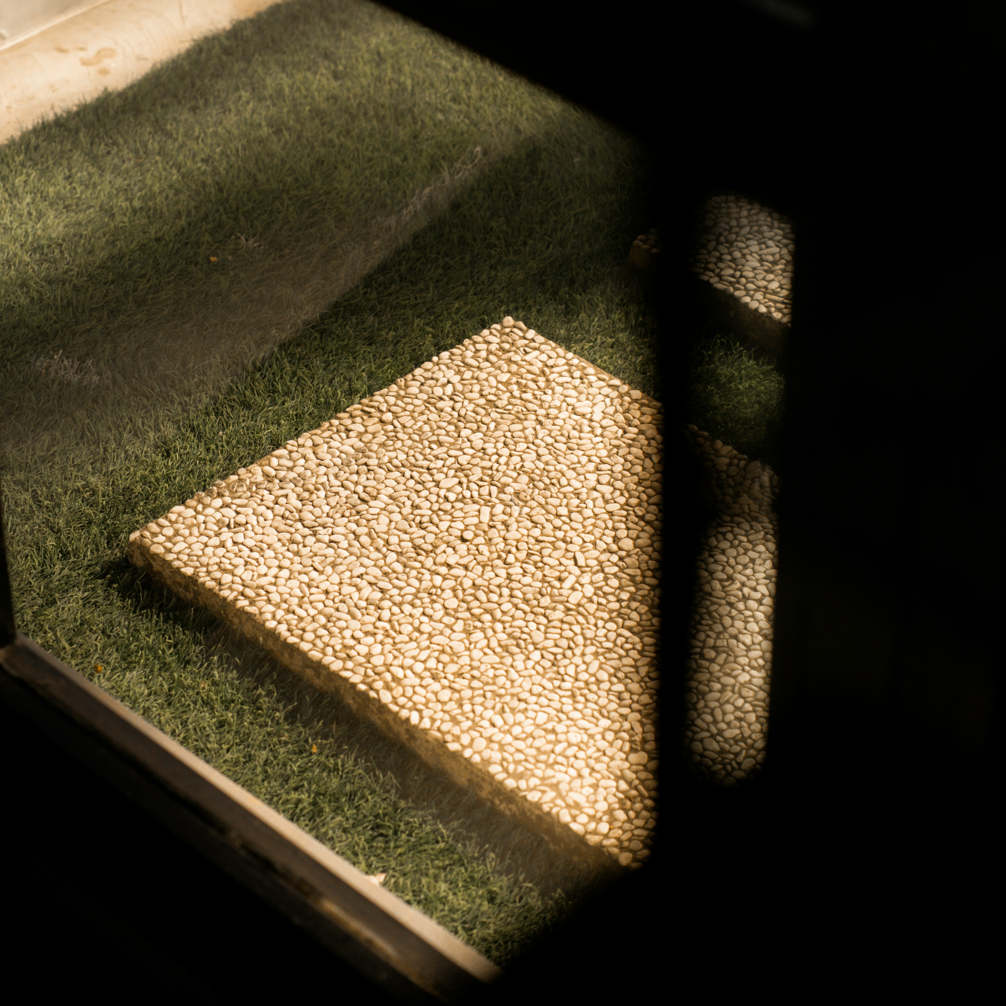 A serene view of a stone pathway bordered by lush artificial grass, showcasing a blend of natural and modern elements.