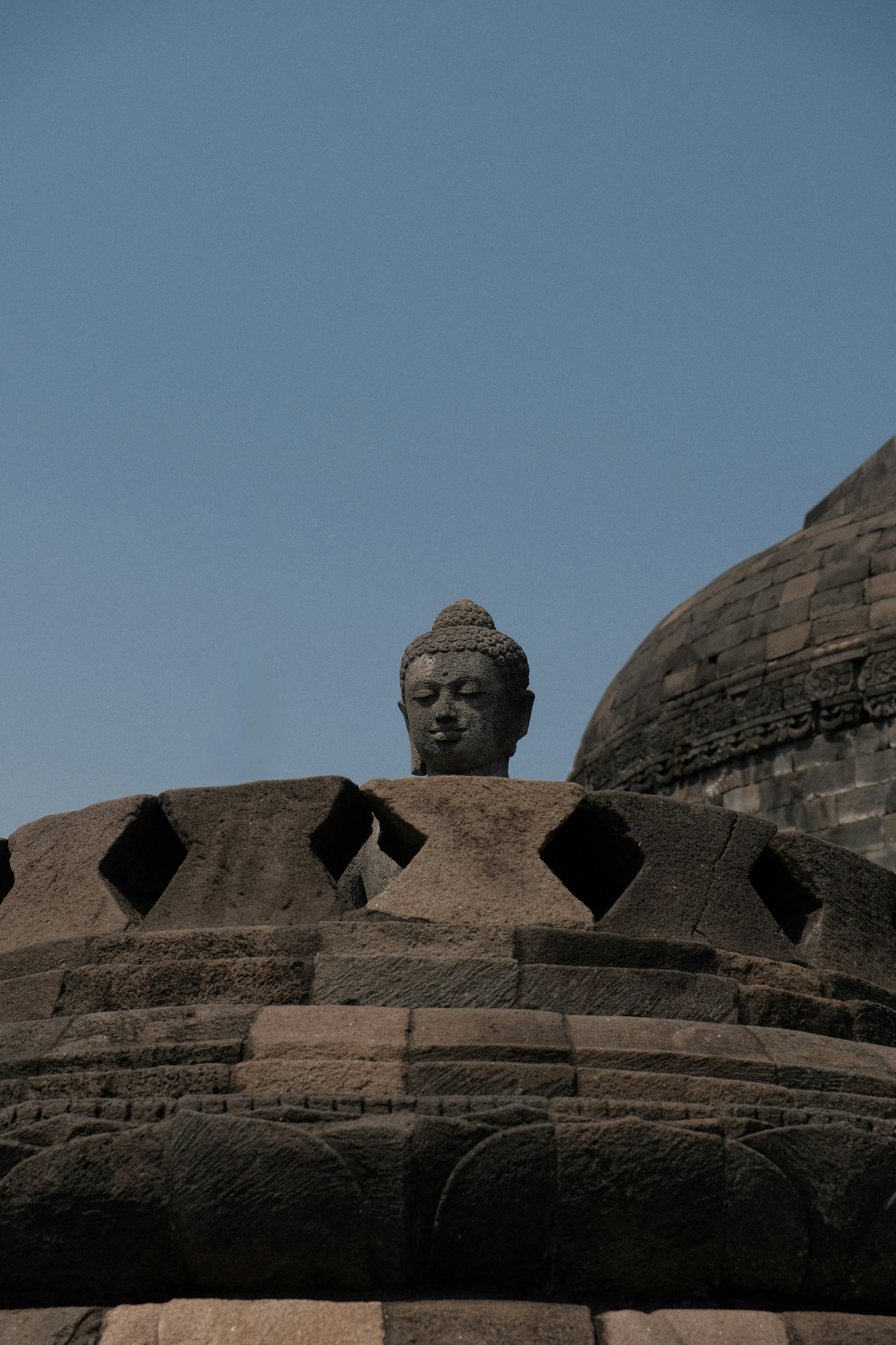 Buddha statue partially visible atop a stone stupa against a clear blue sky.