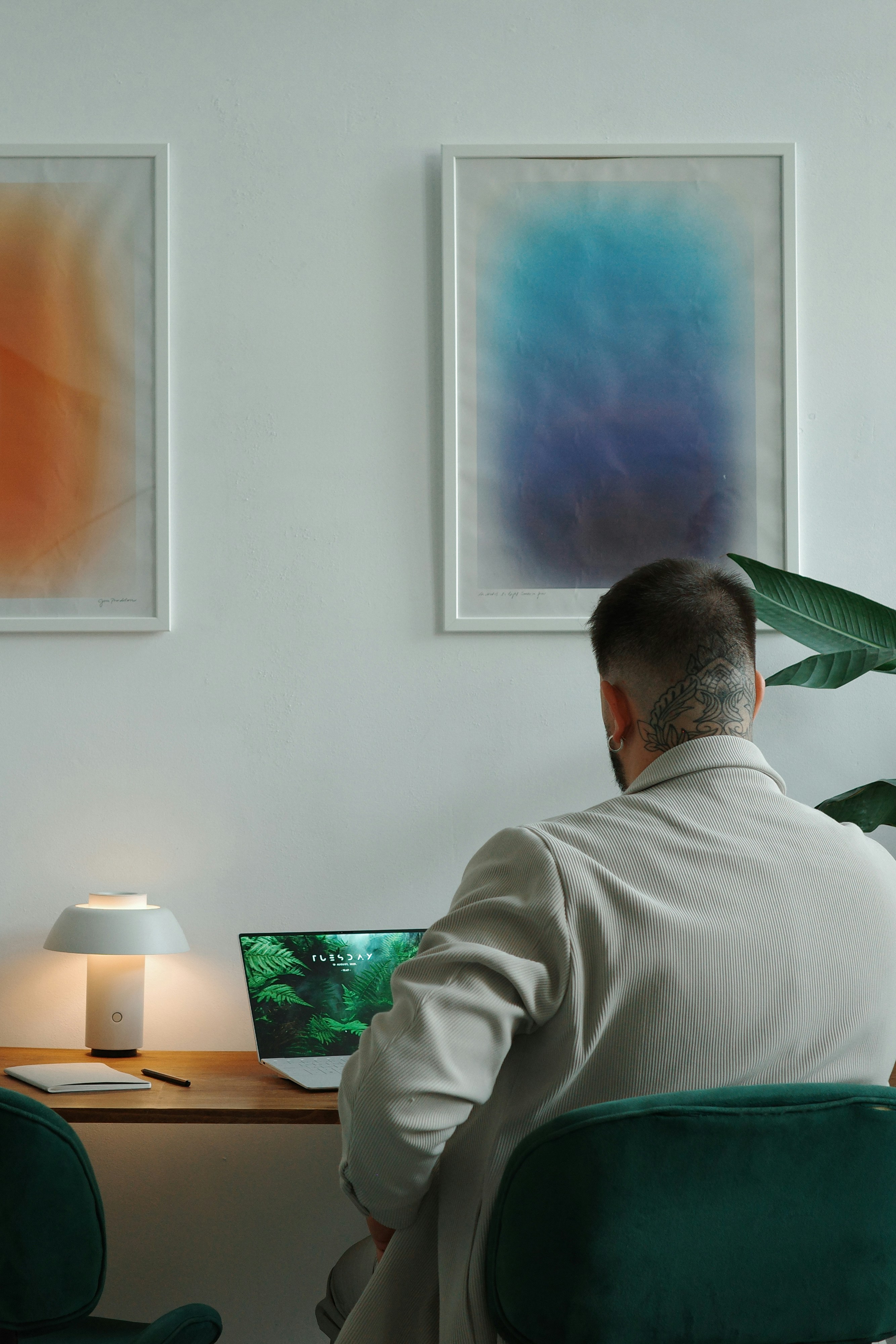 Hombre tatuado trabajando en un ambiente aesthetic con escritorio de madera y un setup minimalista | Man working on laptop in modern office with abstract art