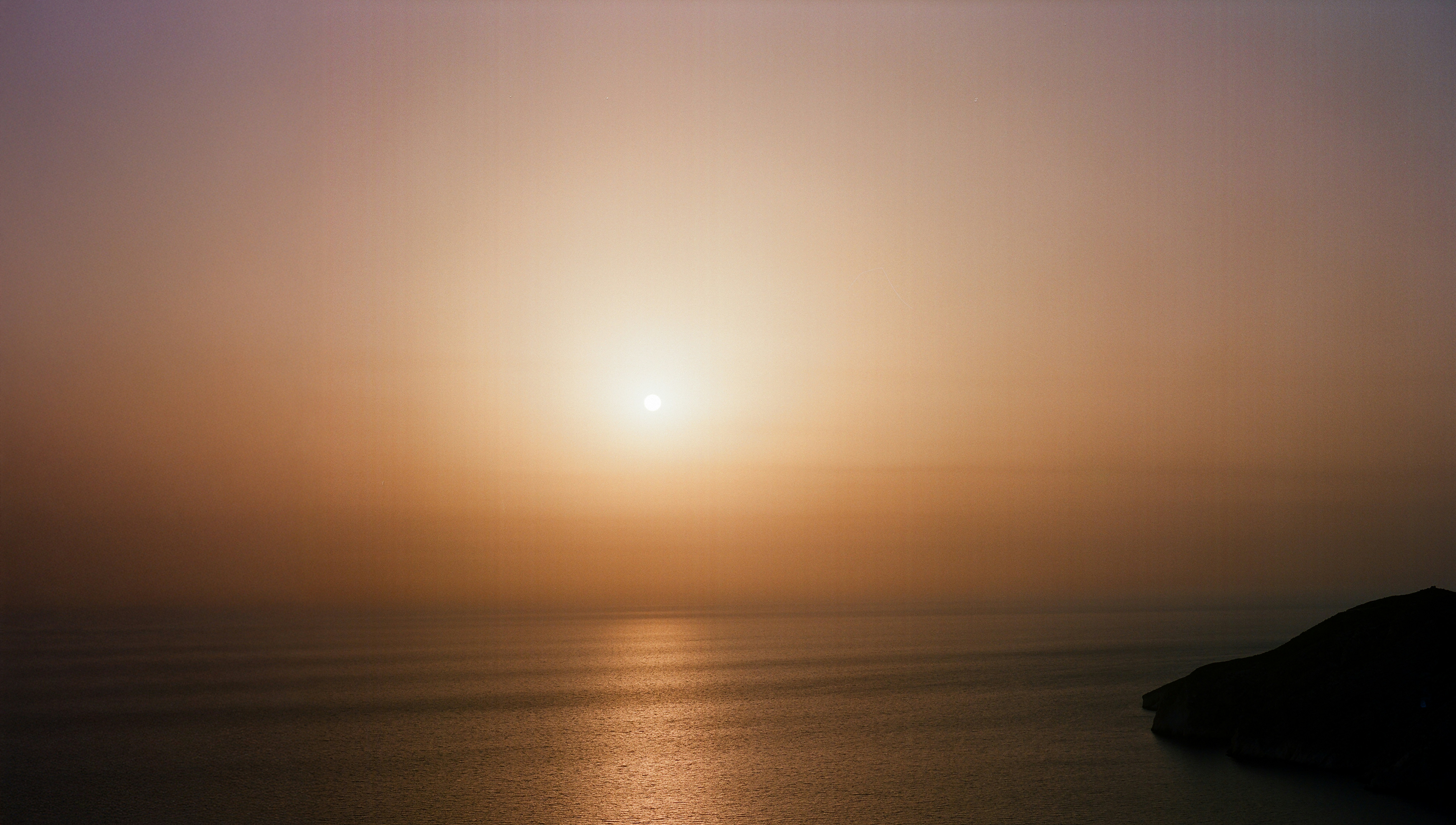 Sunset over the ocean with hazy sky.