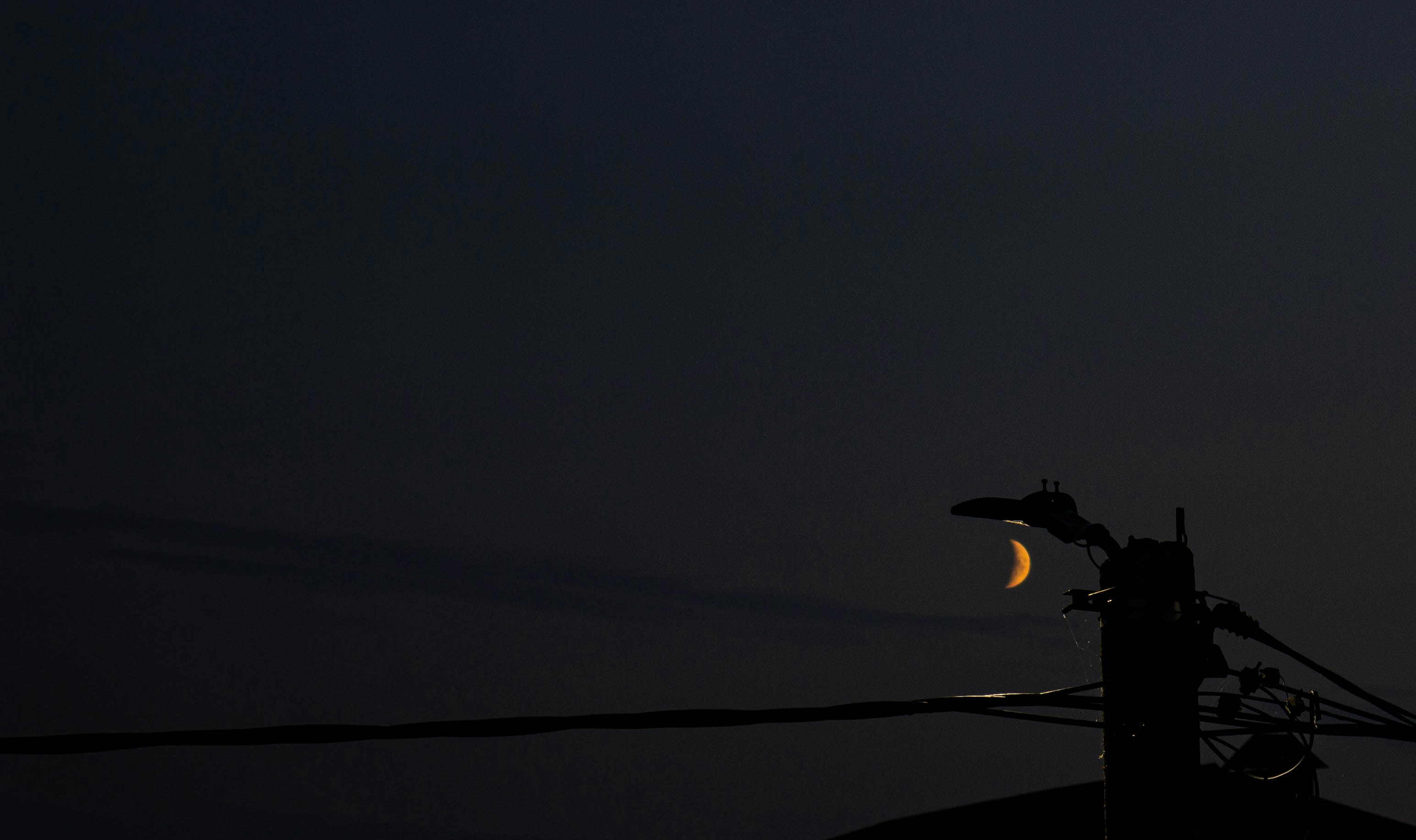 Crescent moon visible behind a street lamp at night