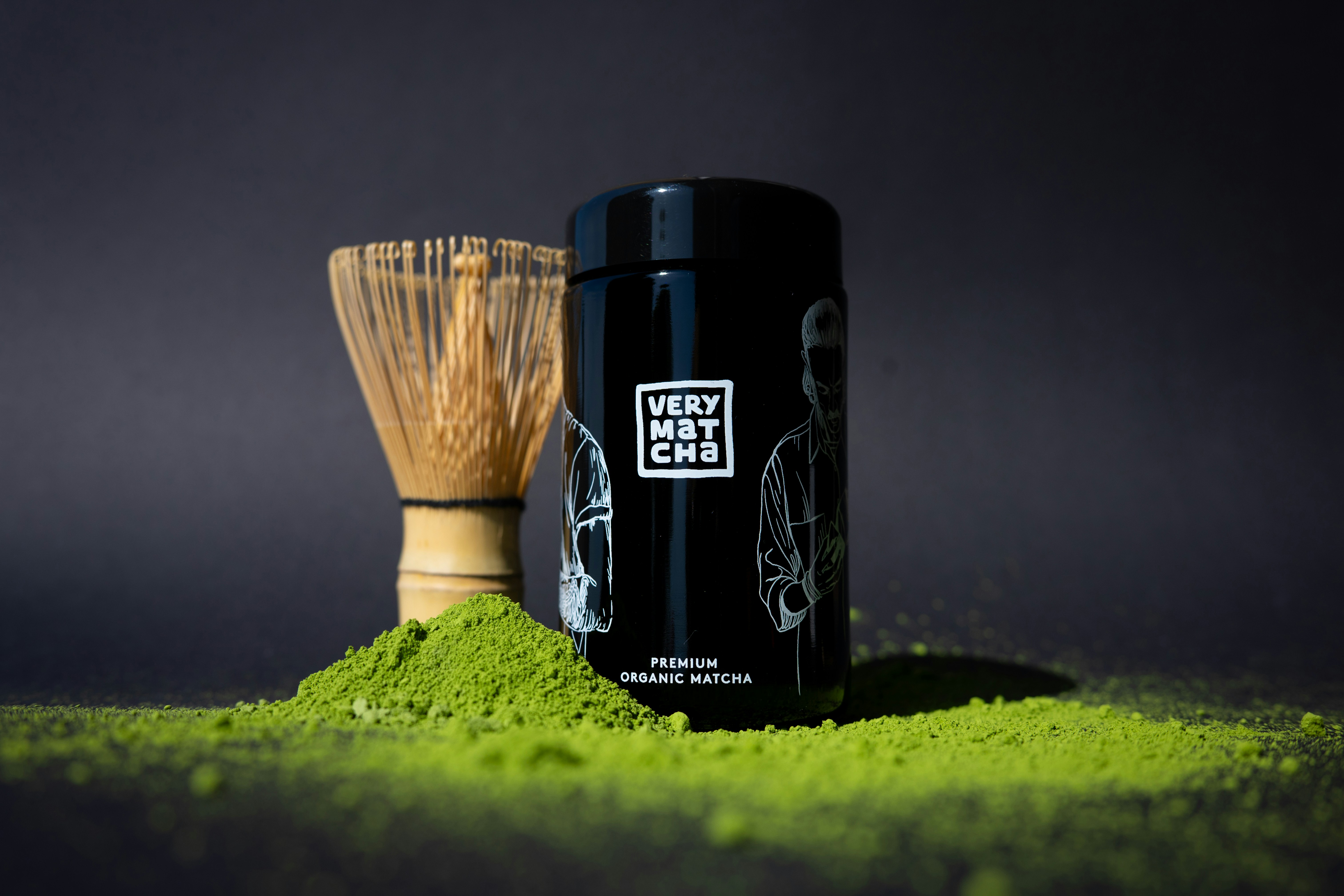 Organic Matcha powder with bamboo whisk (chasen) and black violet glass Very Matcha jar on a dark background. | Matcha powder and whisk on dark background