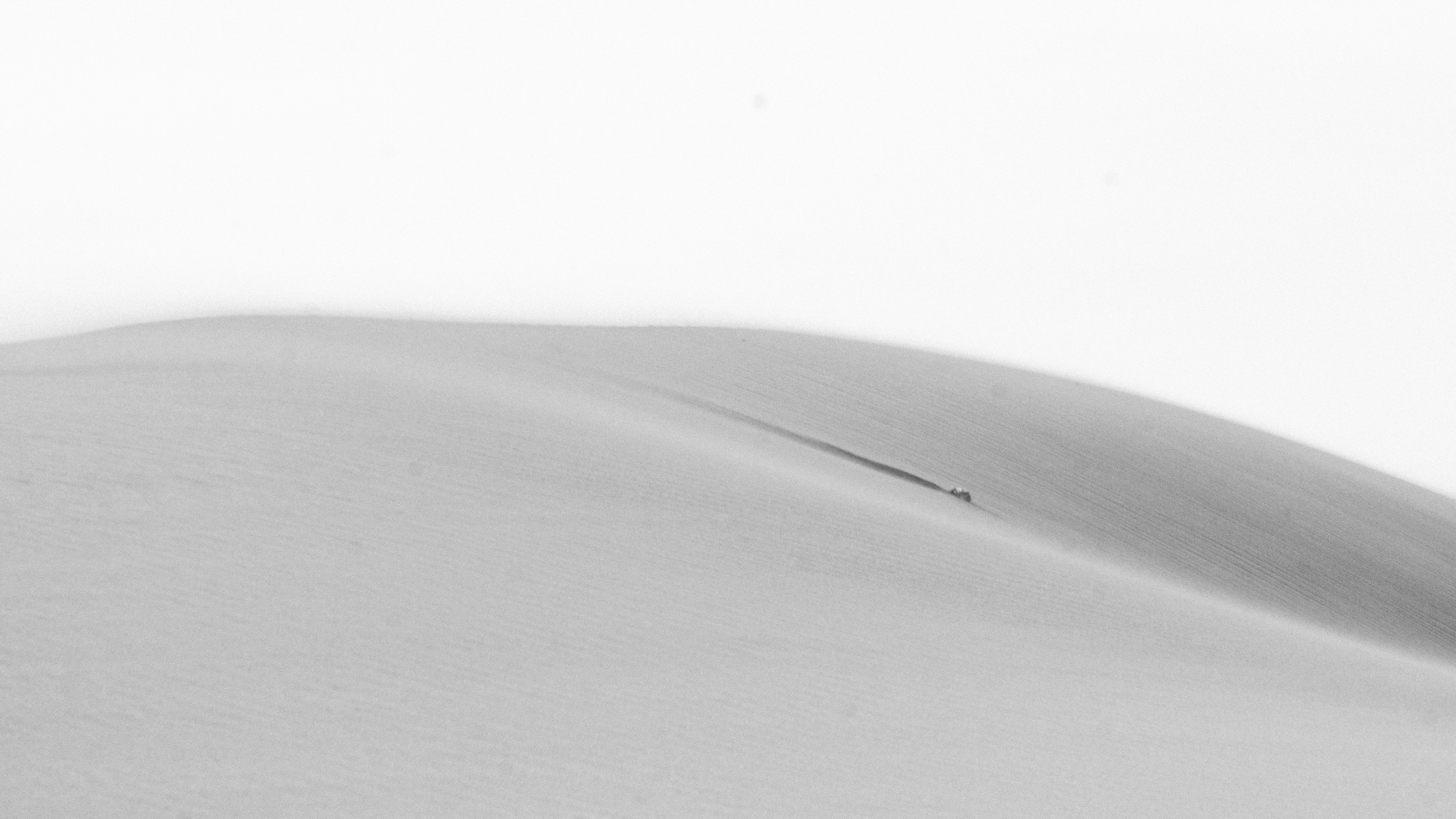 A solitary figure traverses the smooth, undulating surface of a vast desert landscape, evoking a sense of isolation and tranquility.