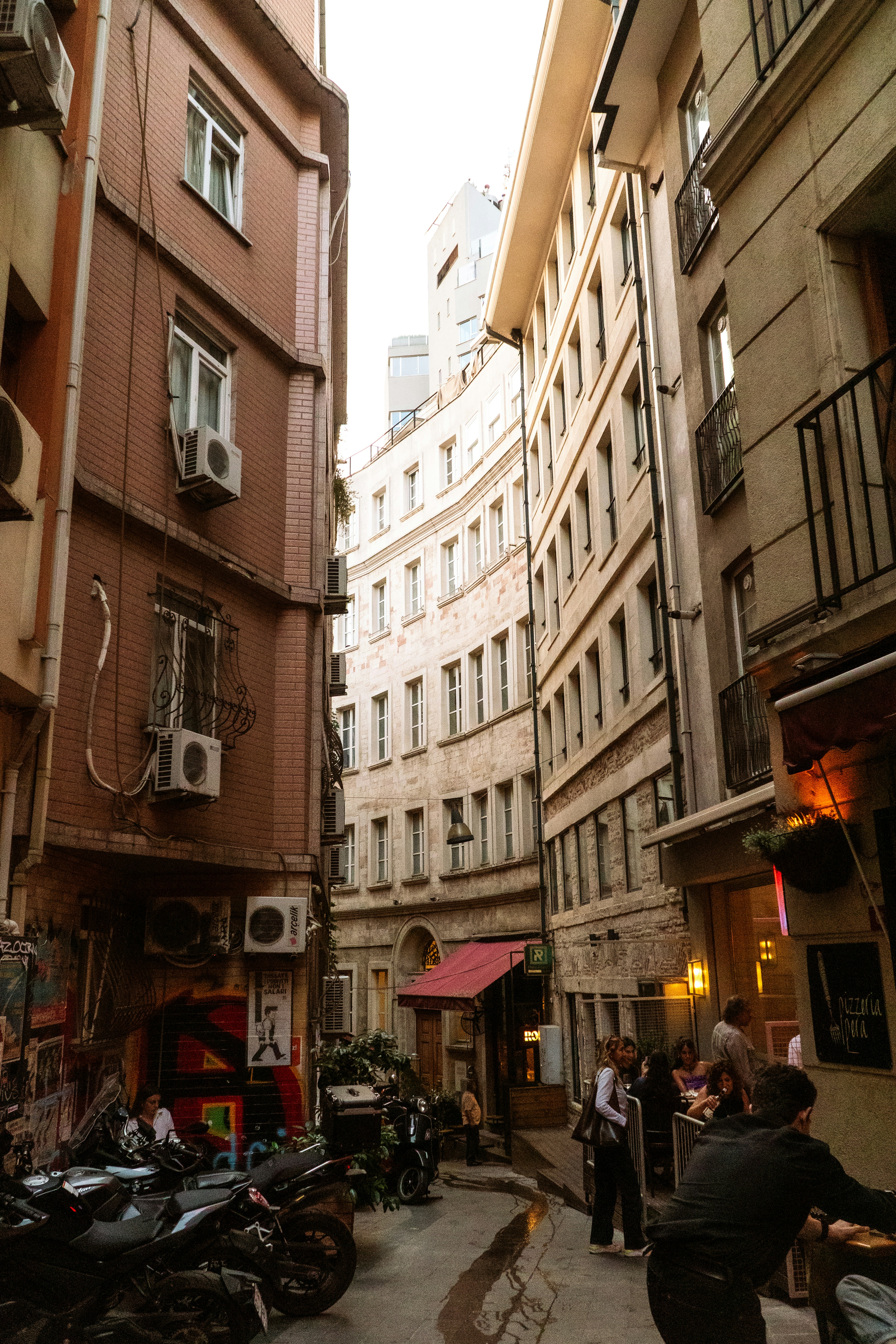Narrow Streets of İstanbul's Vibrant Beyoğlu District | Narrow street between tall buildings with people and motorcycles
