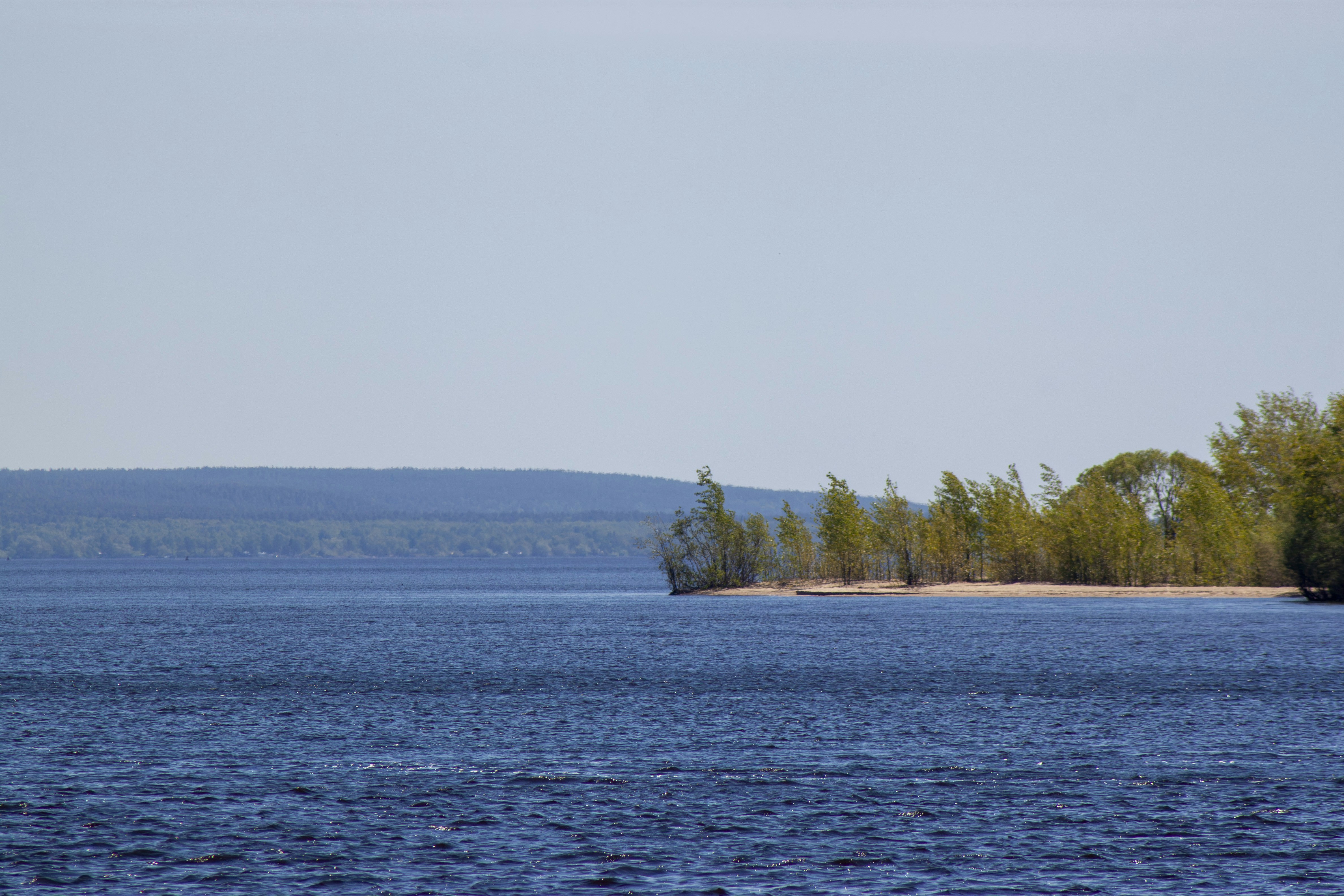 Calm blue lake with a tree-lined sandy shore