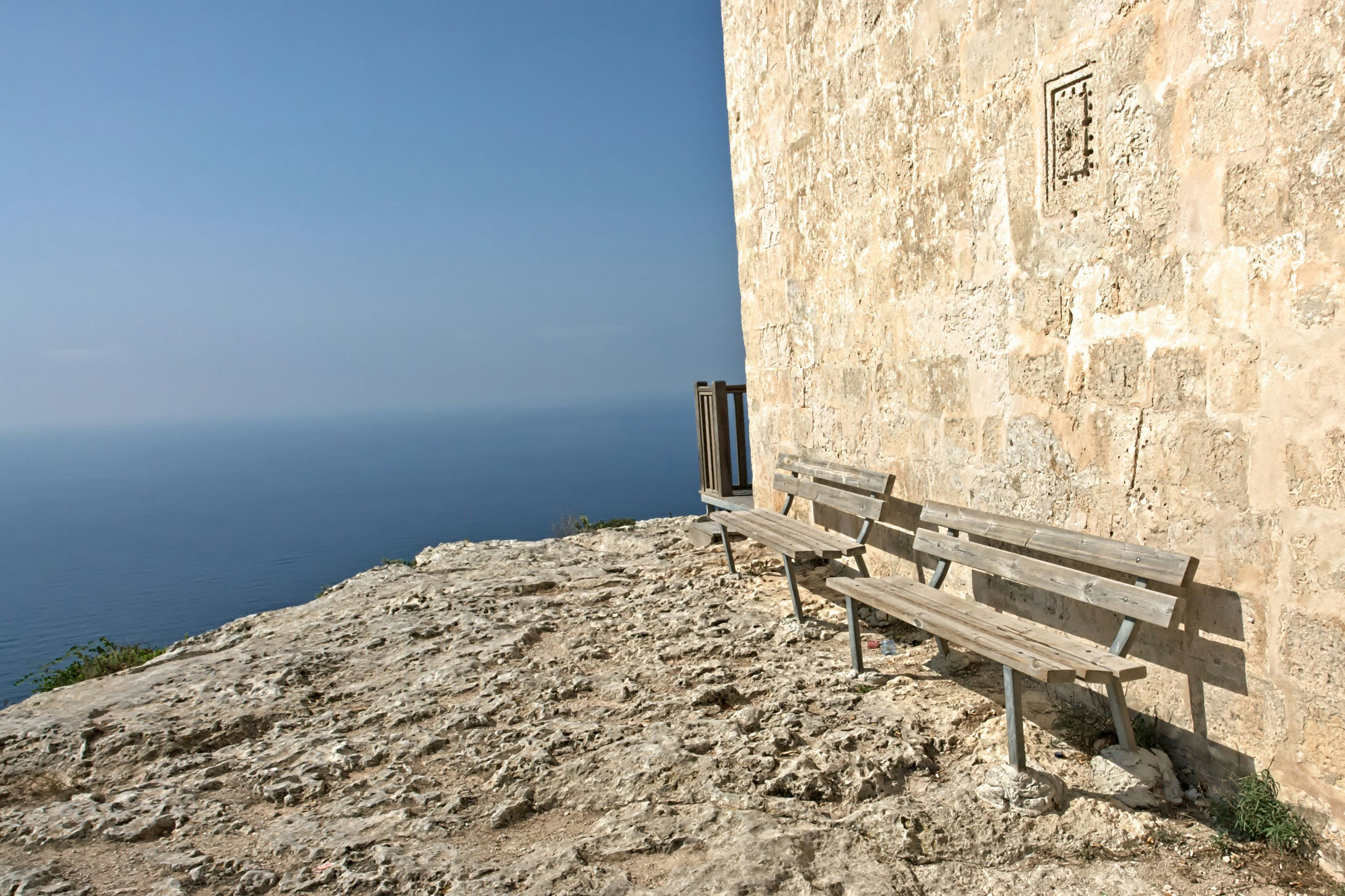 Two wooden benches on a stone patio overlooking the ocean
