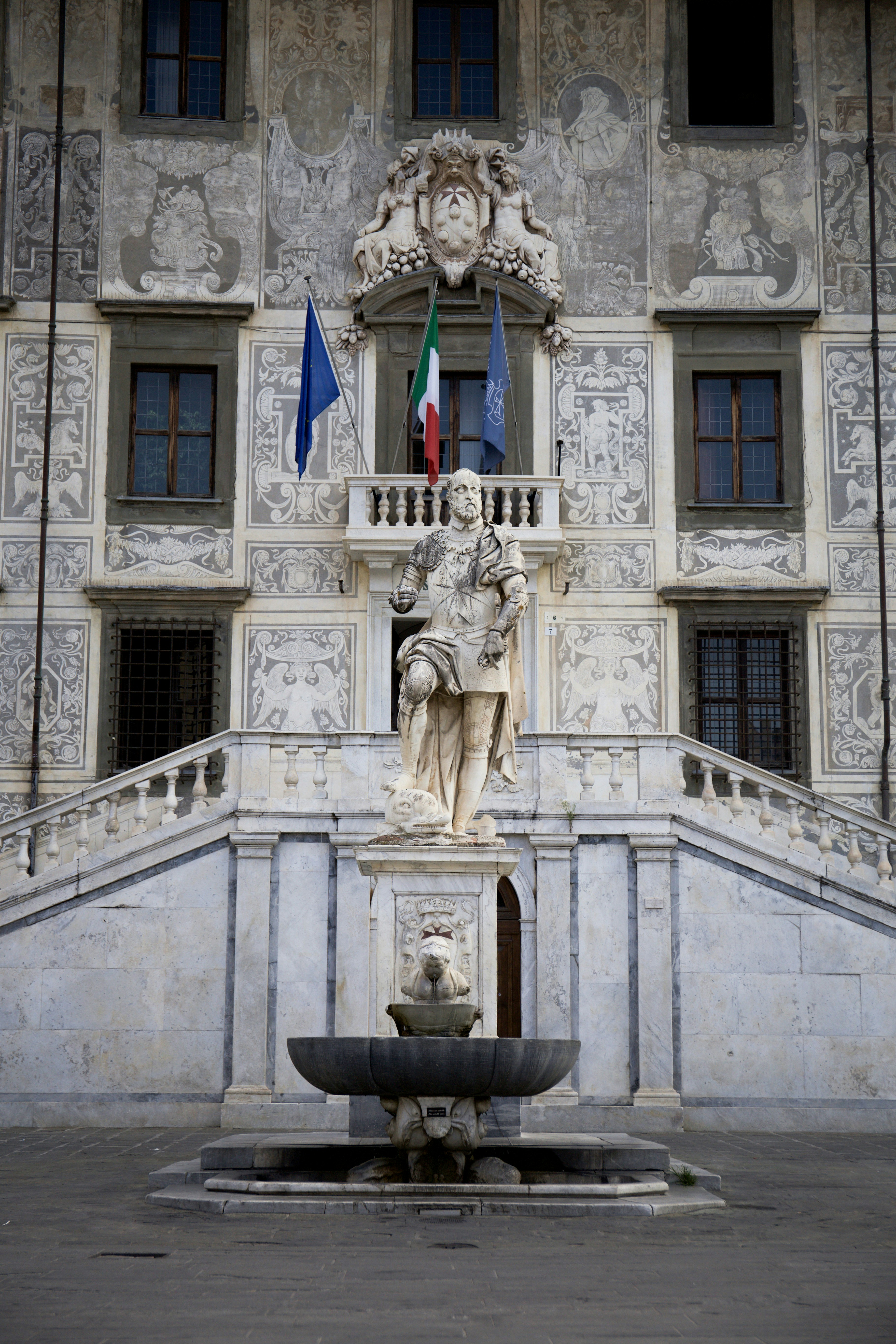 Centerpiece in Stone: Marble Statue Over a Tiered Fountain Against an Ornate Frescoed Facade