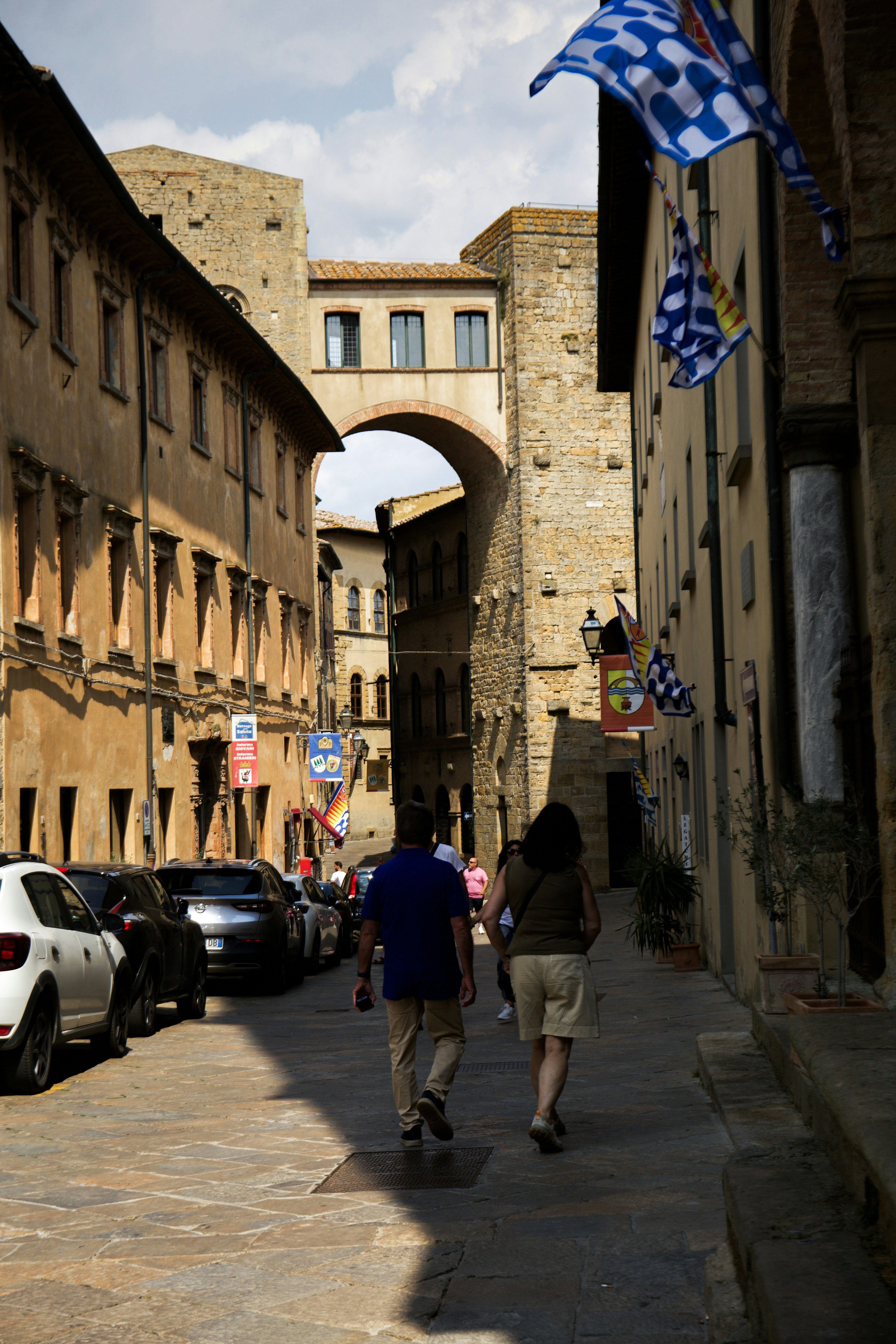 People walk down a cobblestone street with old buildings.